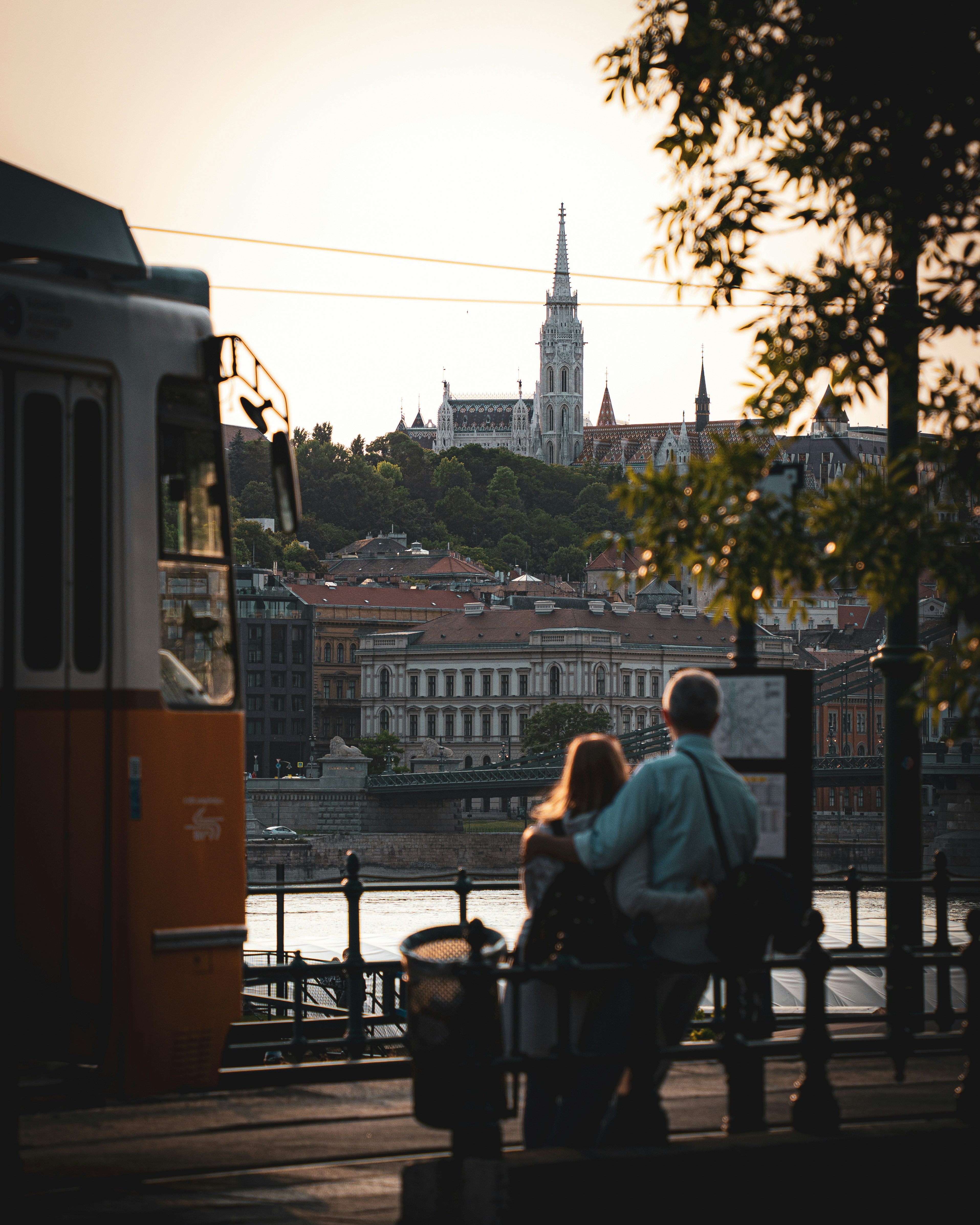 Couple at the Riverfront Tracing the Cityscape under a Dusk-tinted Tram