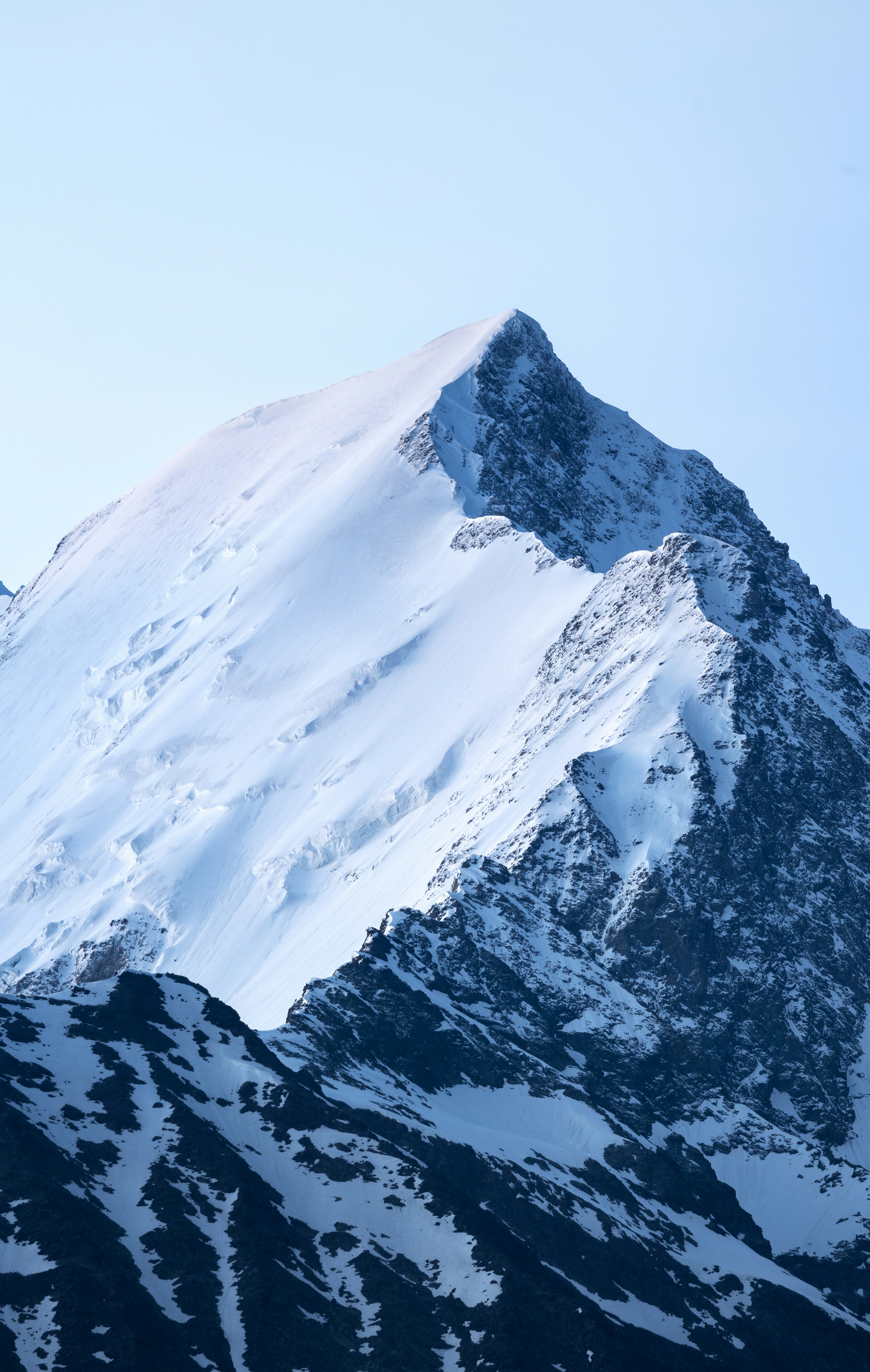 Snow-covered mountain peak rising majestically against a pale sky, showcasing rugged terrain and gleaming ice.