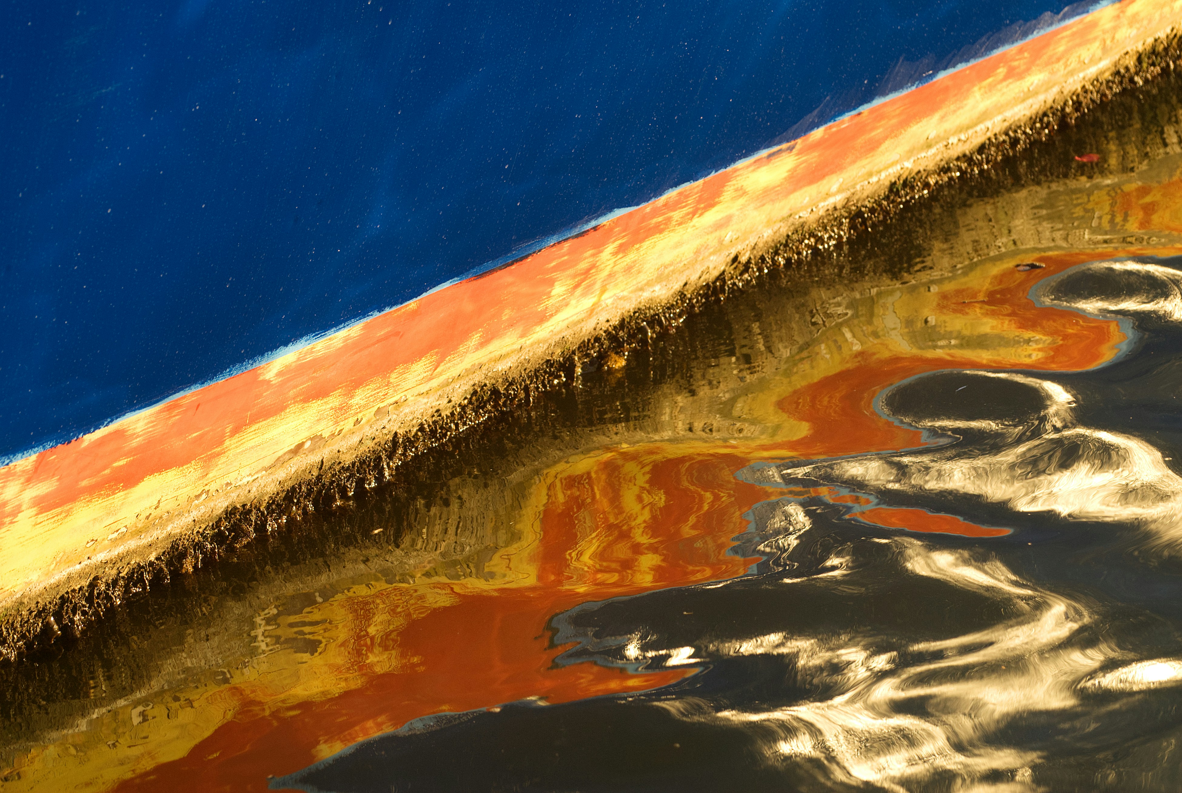 Vibrant colors and textures of a boat's hull reflected in the water, showcasing a blend of blue, orange, and gold hues.