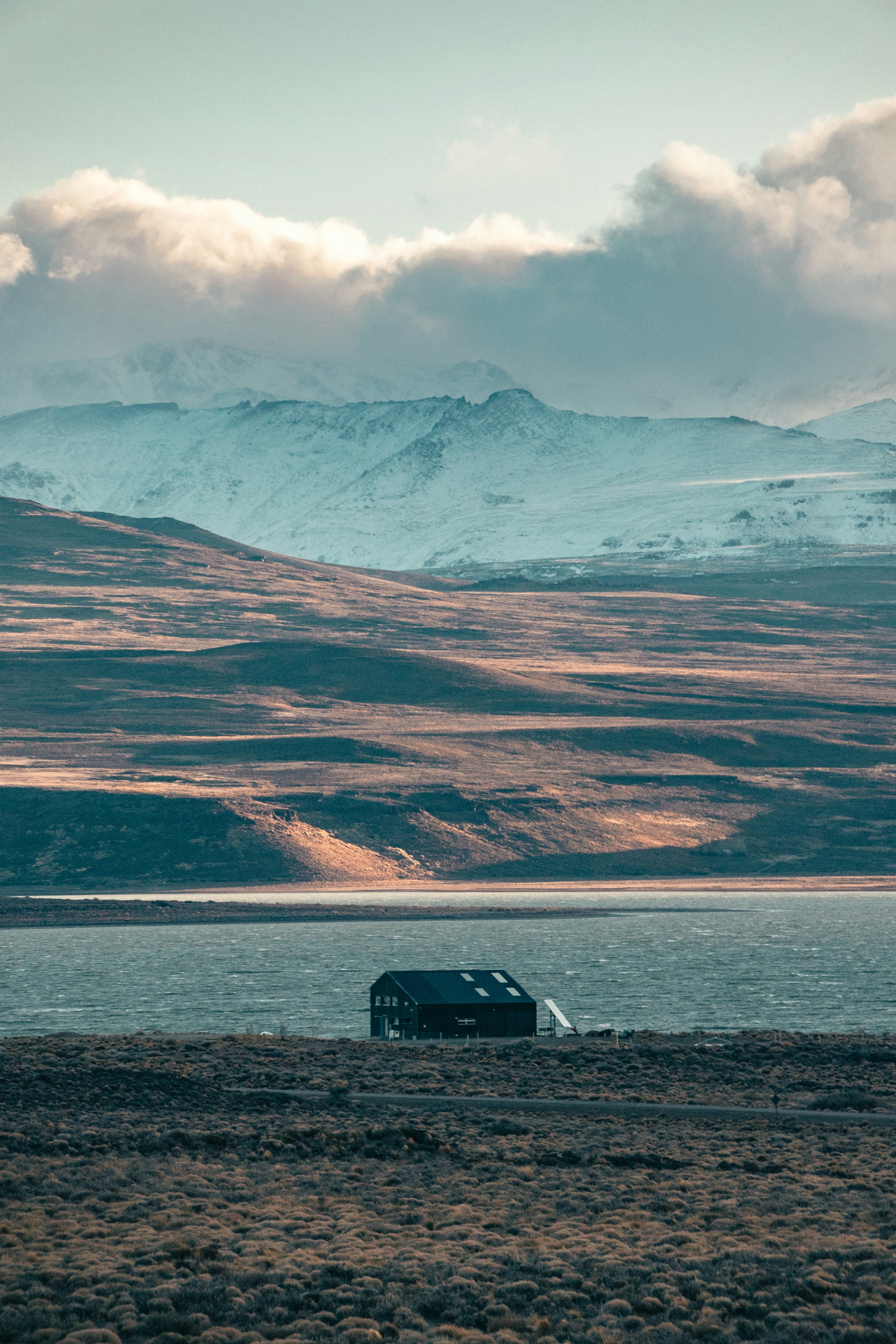 A lonely cabin sits by the vast, cloudy lake.