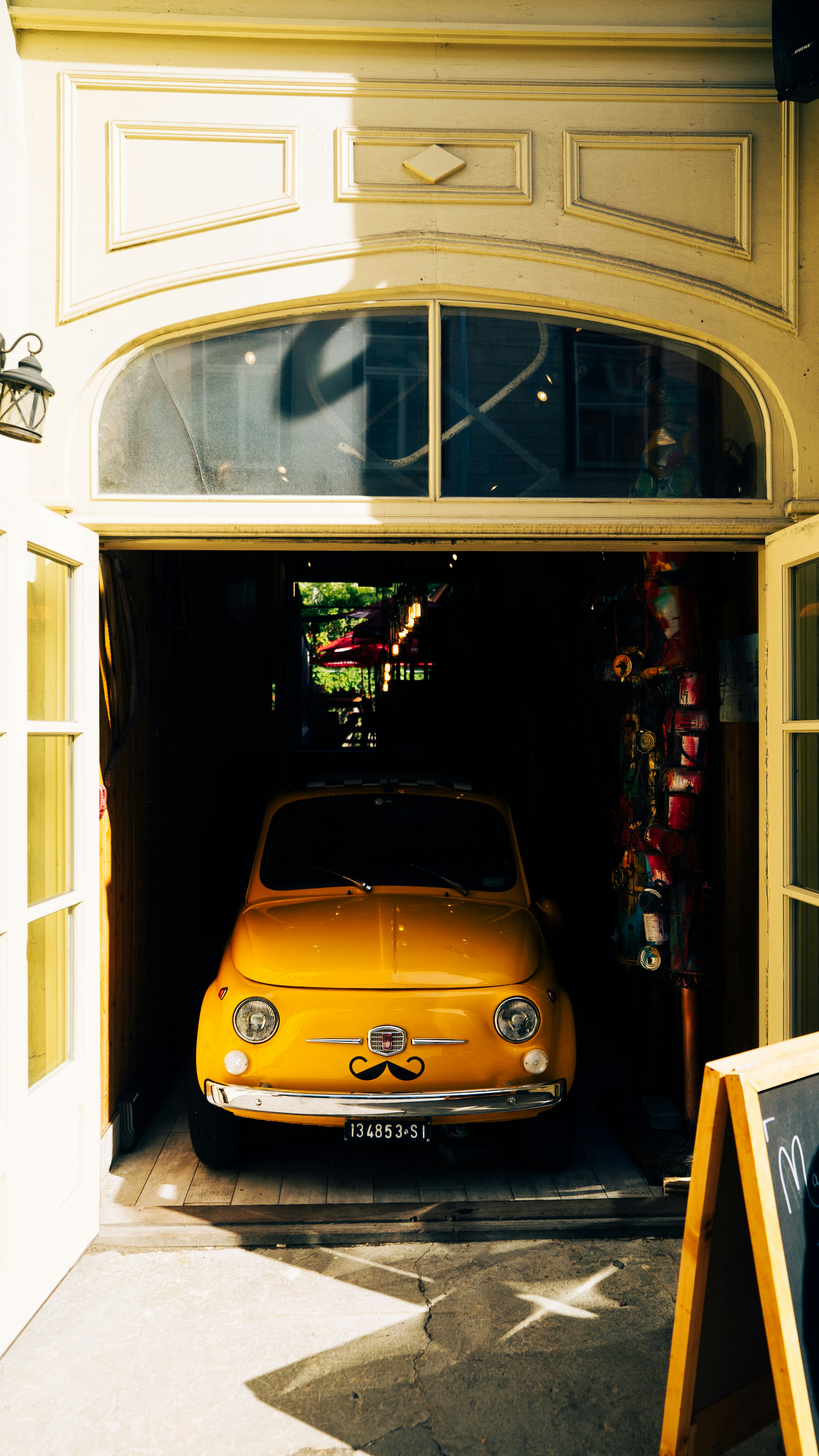 Bright yellow vintage car peeking out from a dimly lit passageway adorned with colorful decorations.