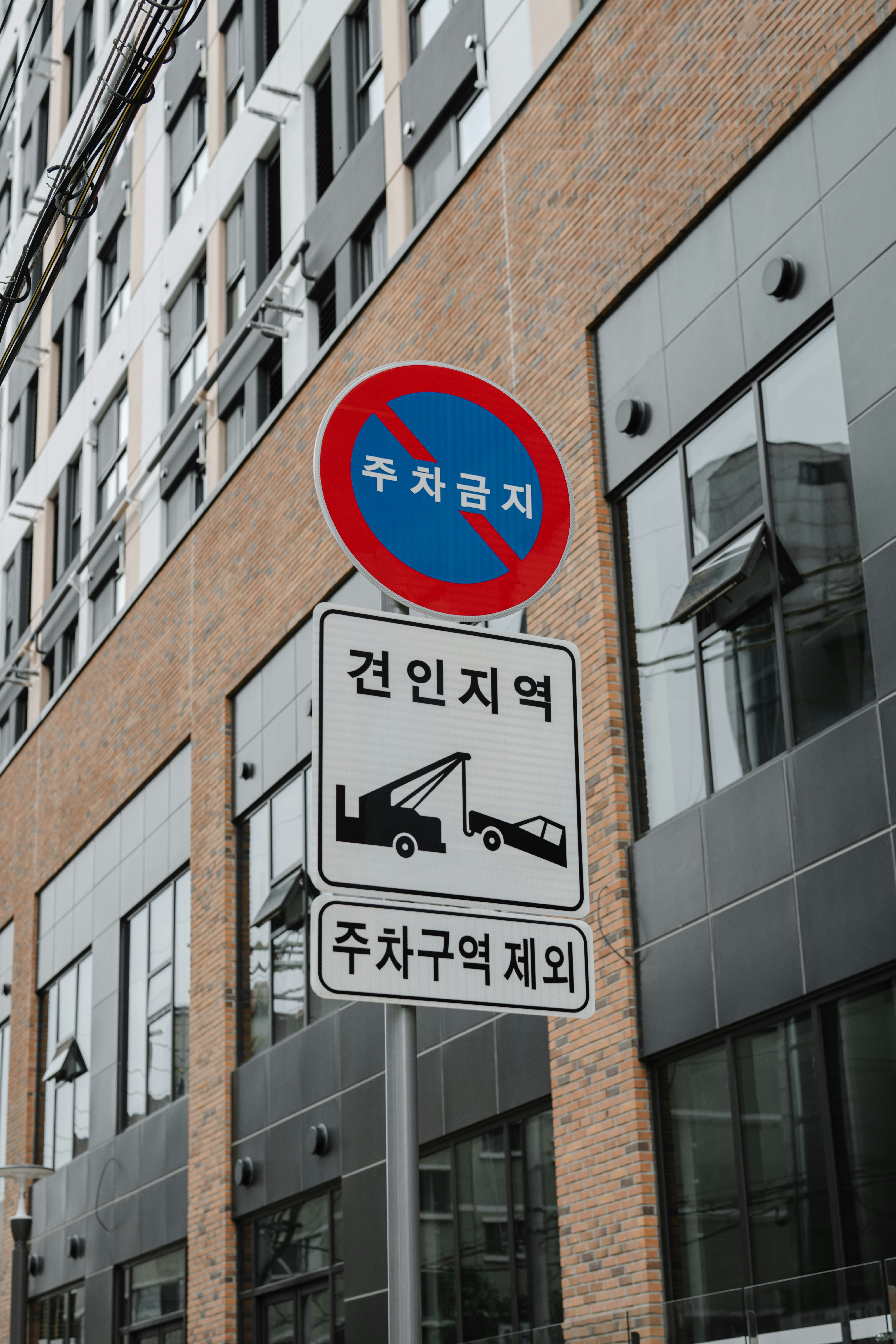 Traffic signs indicating no parking and towing areas near modern buildings in an urban setting.