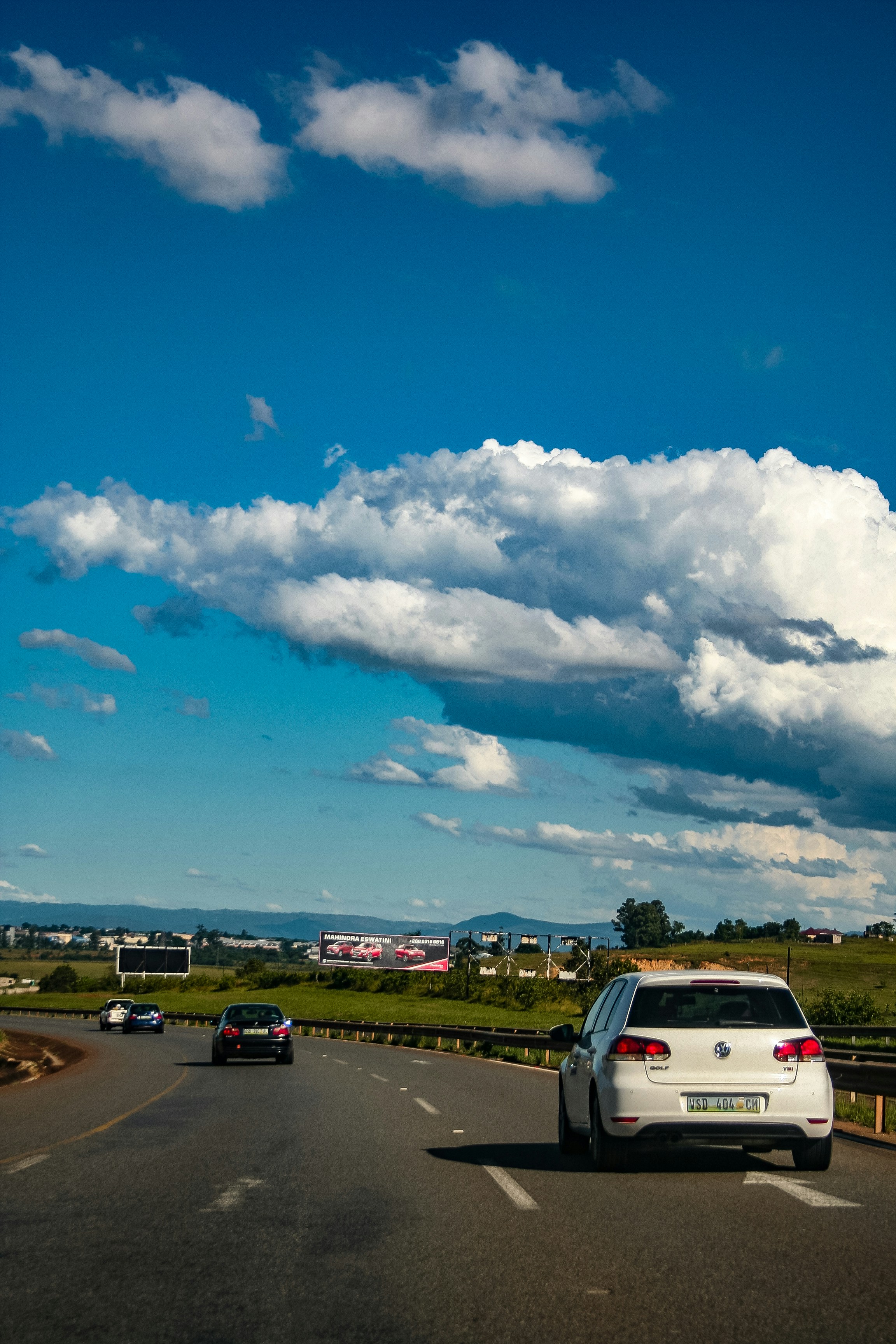 White SUV on a sunlit highway beneath a sweeping cloudscape