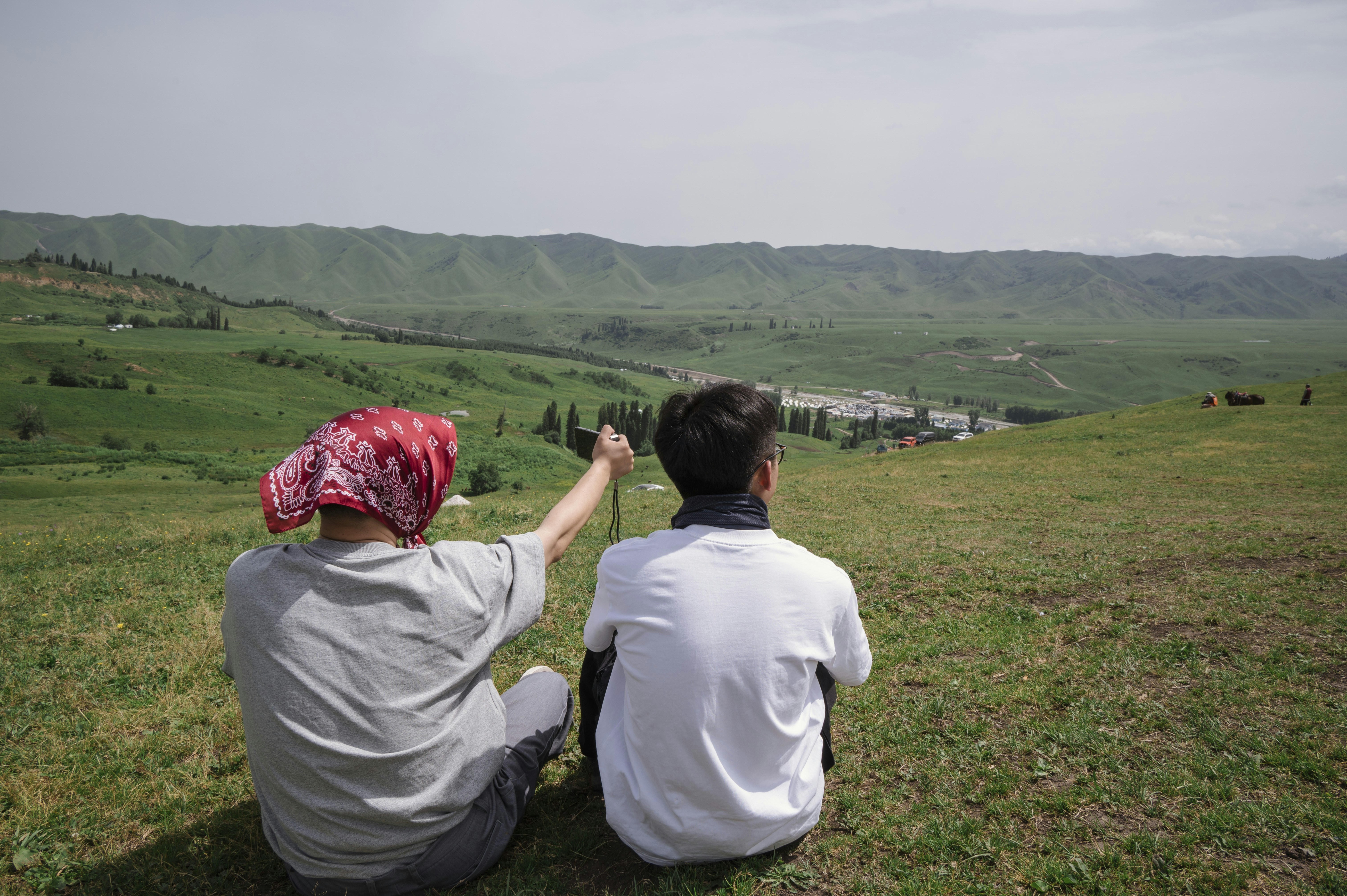 Two hikers on a sunlit hillside overlook a distant valley