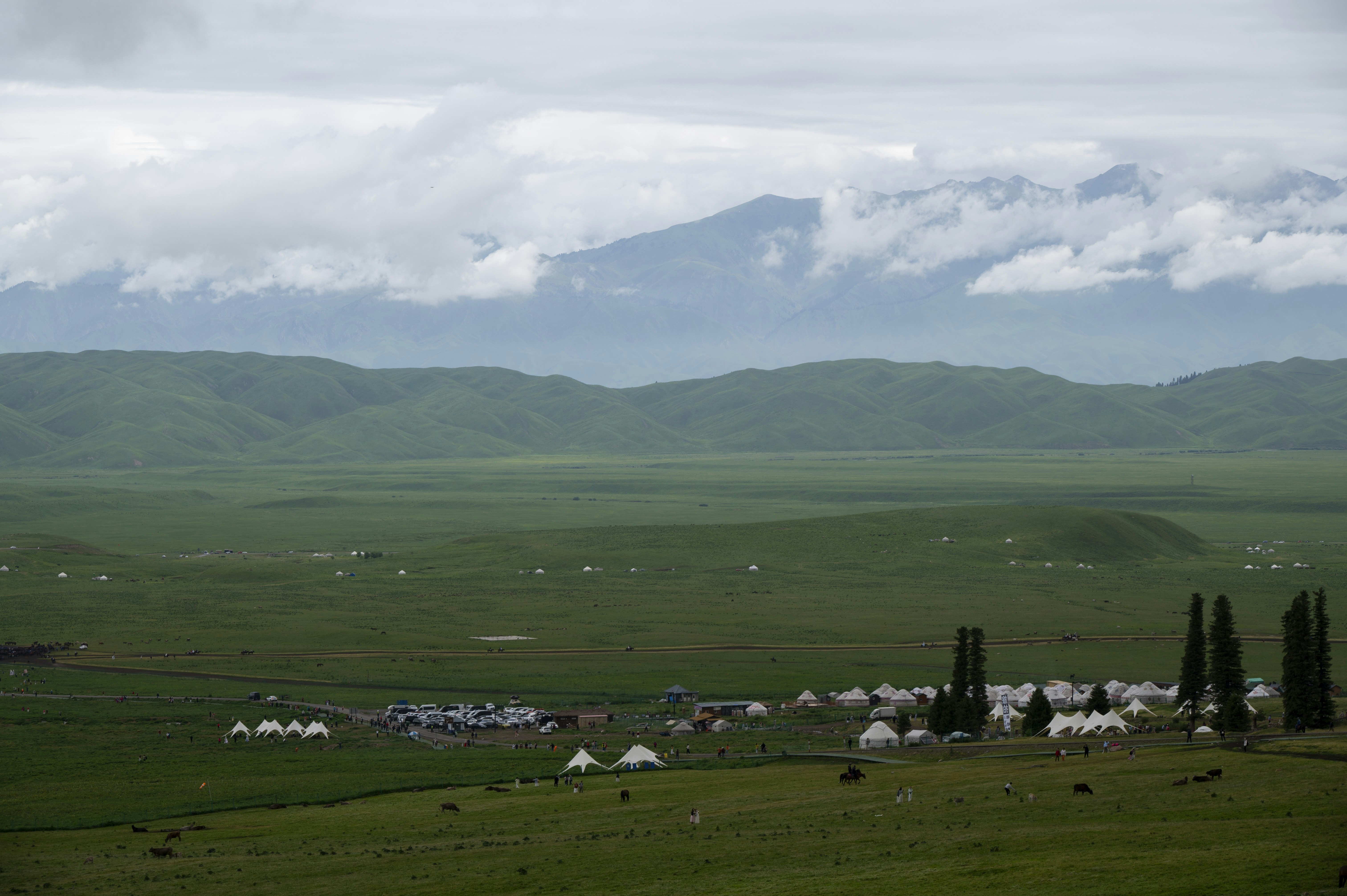 Expansive green steppe dotted with traditional yurts, framed by distant mountains under a cloudy sky.