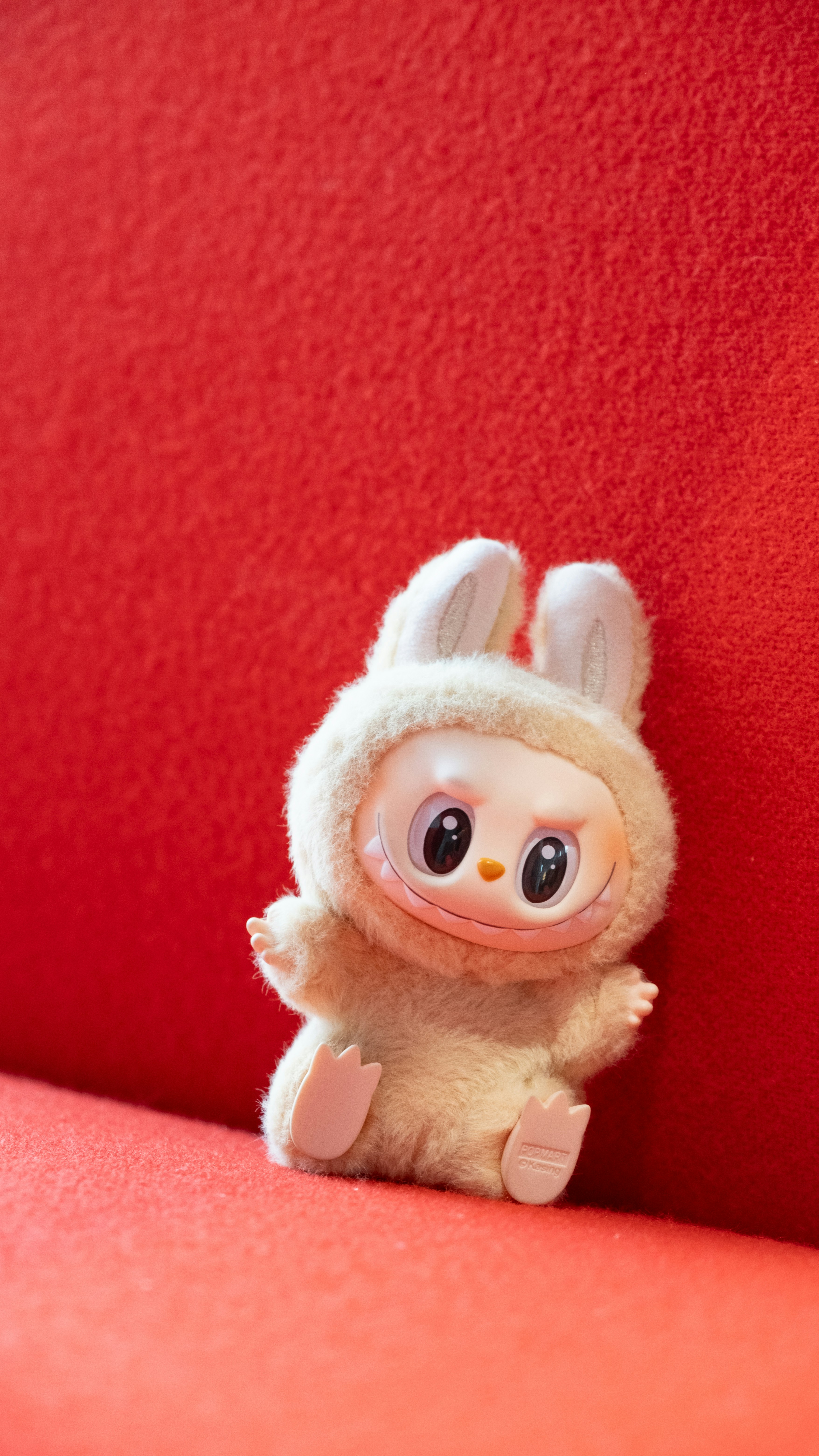 A cute, plush bunny character with large expressive eyes sits on a vibrant red couch, exuding a playful charm.
