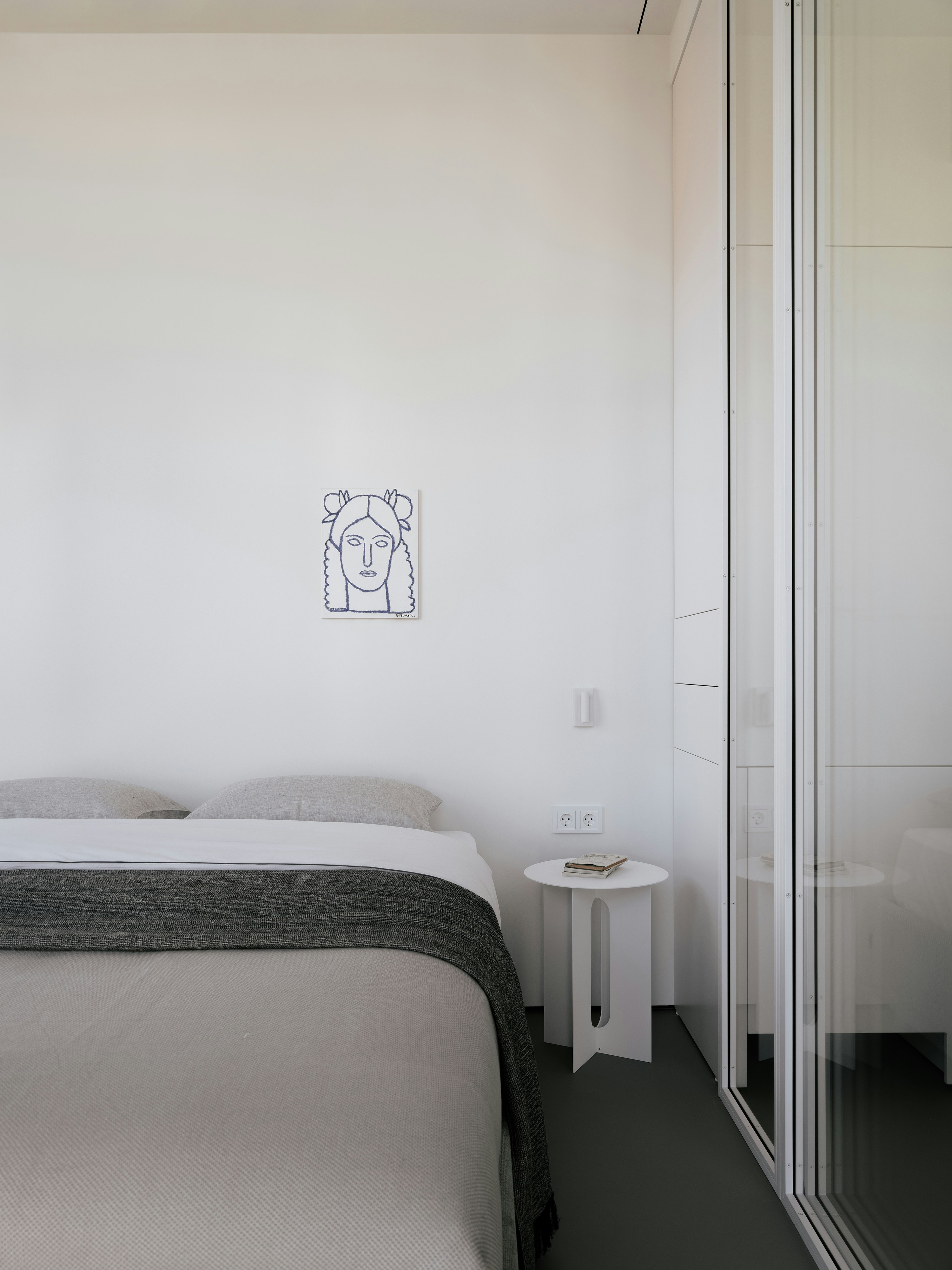 Minimalist bedroom features a bed, art, and a small table.