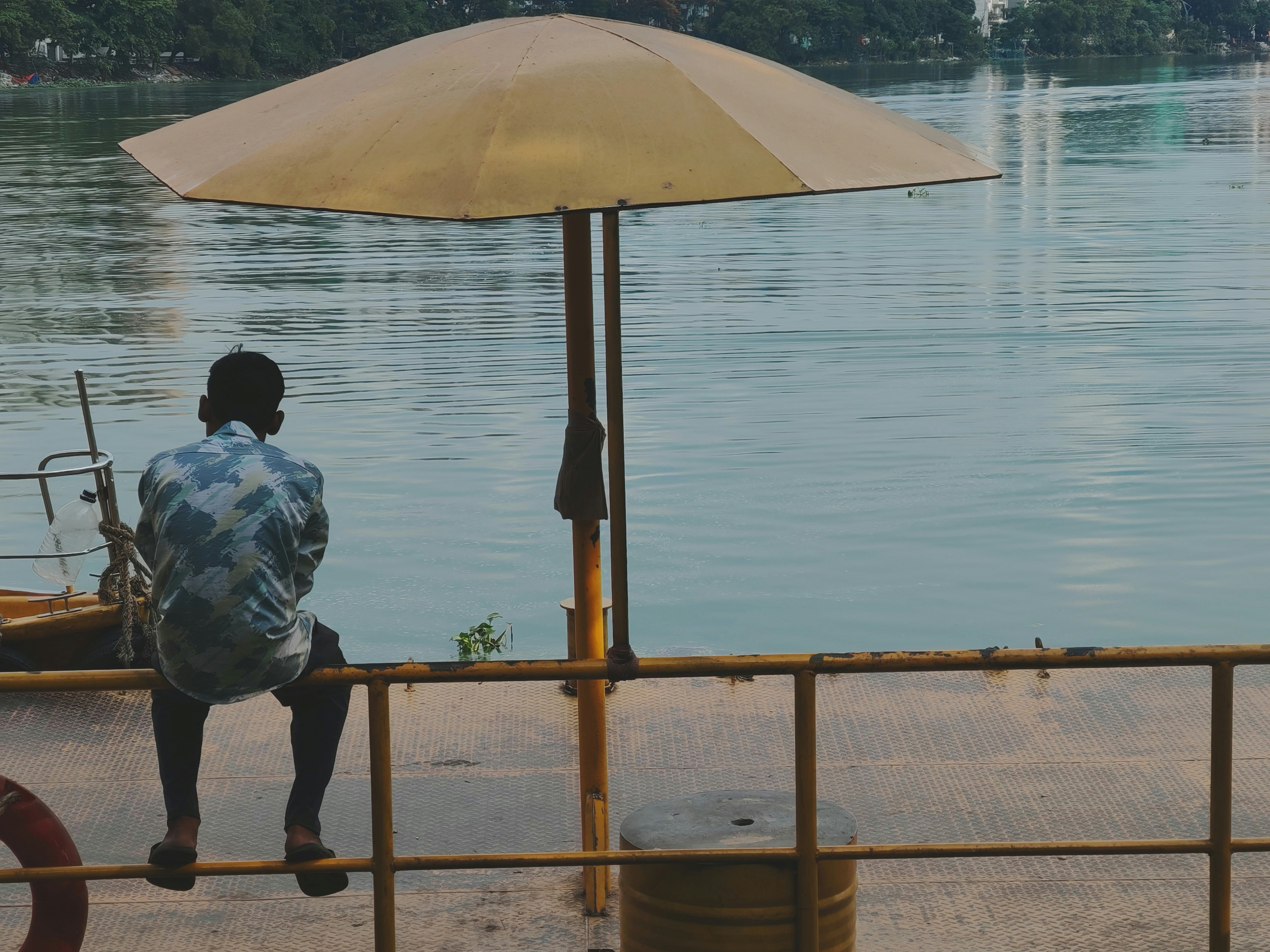A lone figure sits beneath a yellow umbrella, gazing out over a tranquil body of water, embodying a moment of introspection.