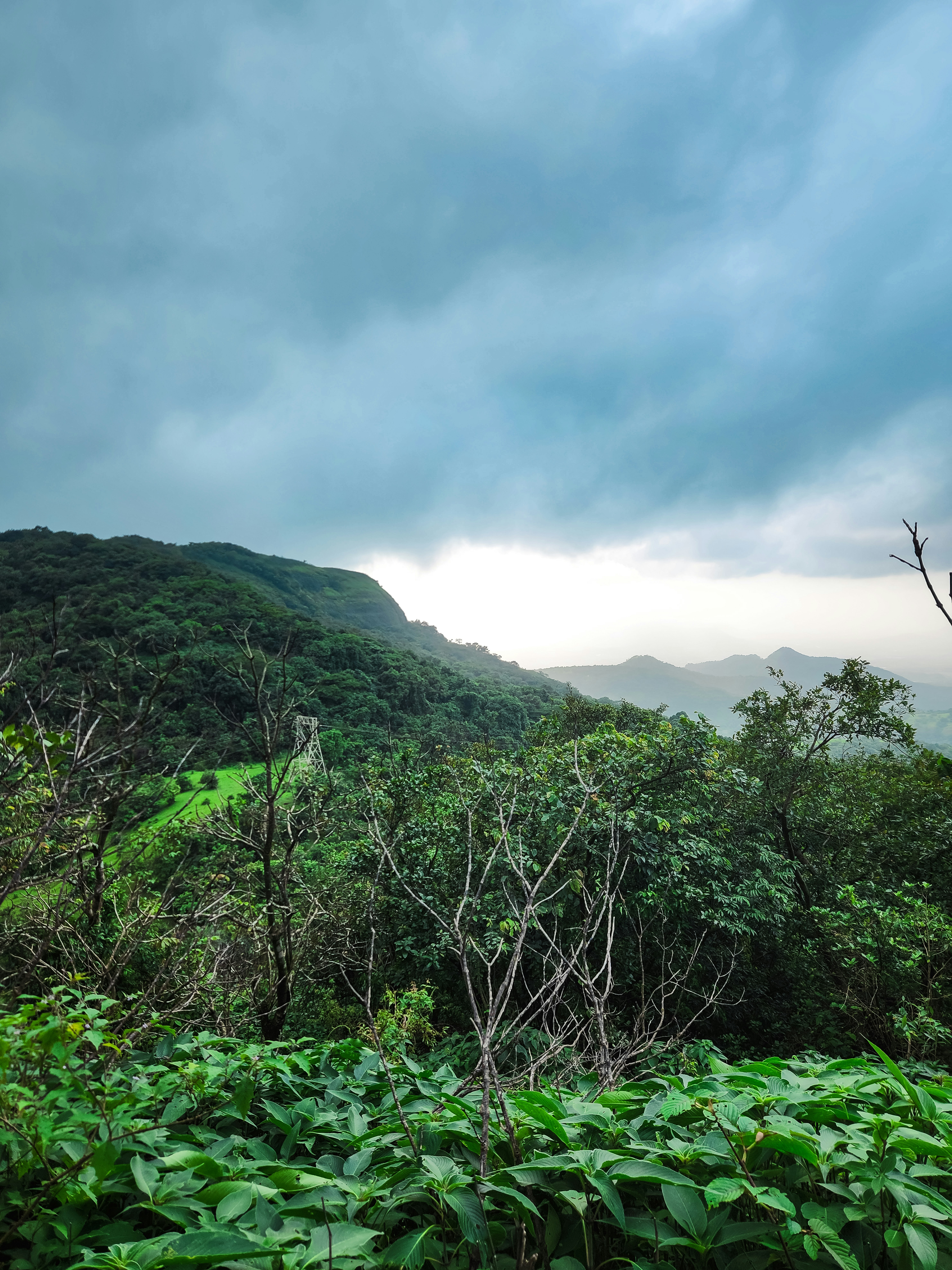 Lush green hills under a brooding sky, with the sun peeking through the clouds in the distance. The scene captures the tranquility of nature's landscape.