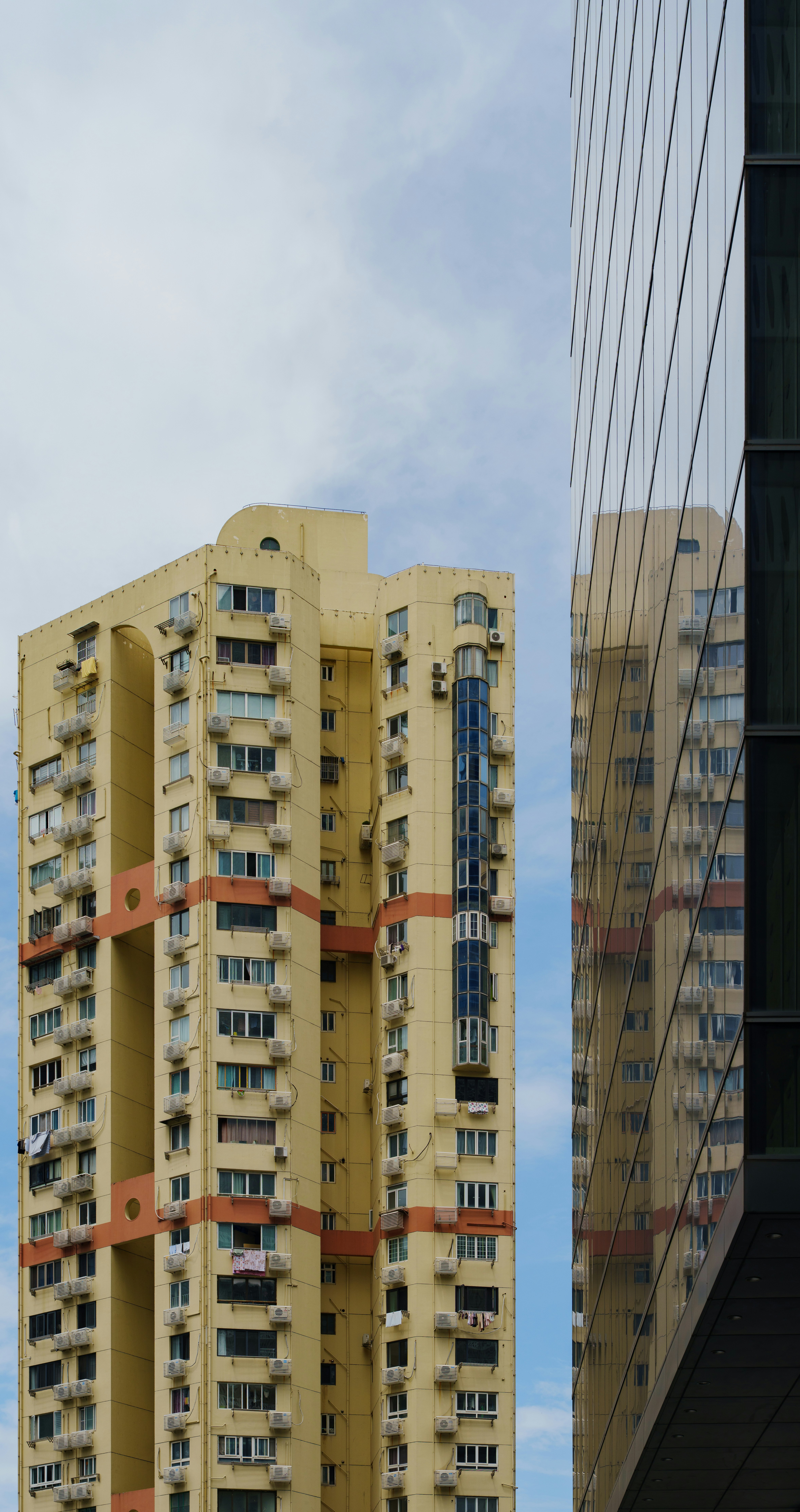 Reflection of apartment building on glass curtain wall | Two buildings stand tall against the sky.