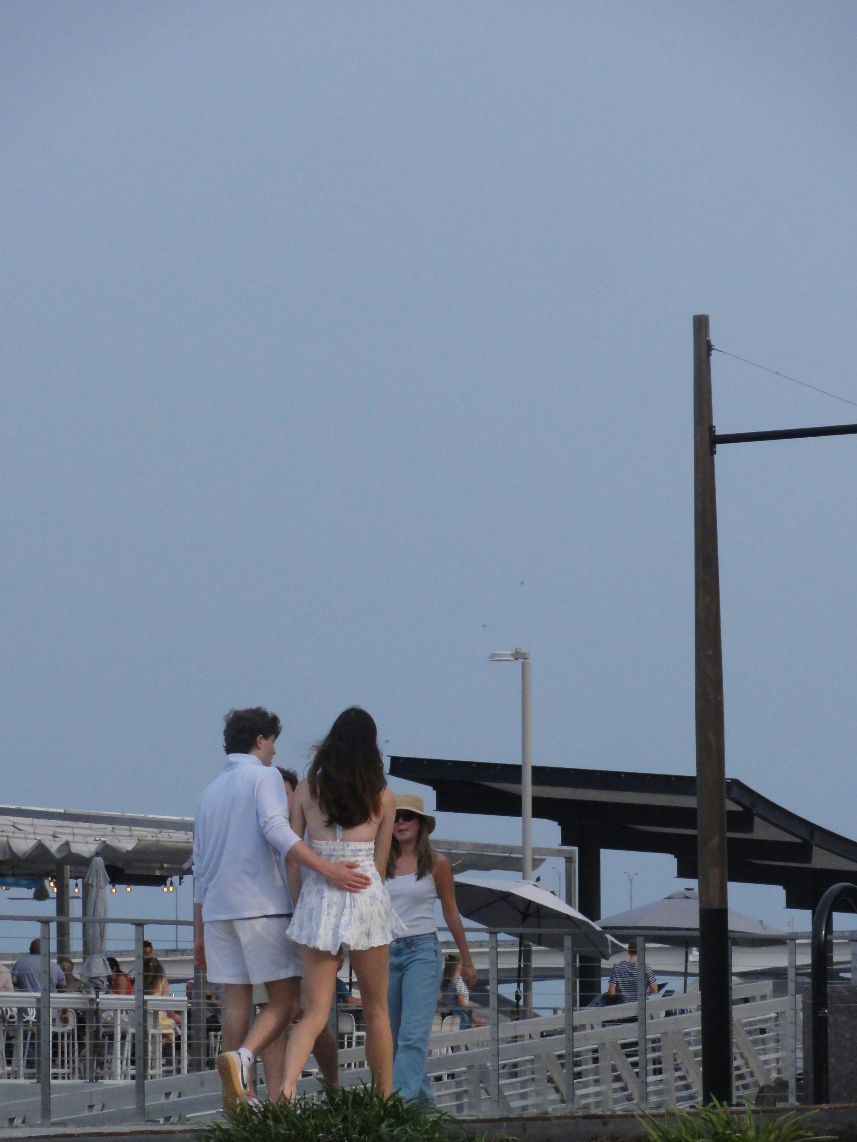 Group of friends enjoying a leisurely walk along the waterfront, dressed in casual summer attire. The scene captures a relaxed atmosphere as they engage in conversation.