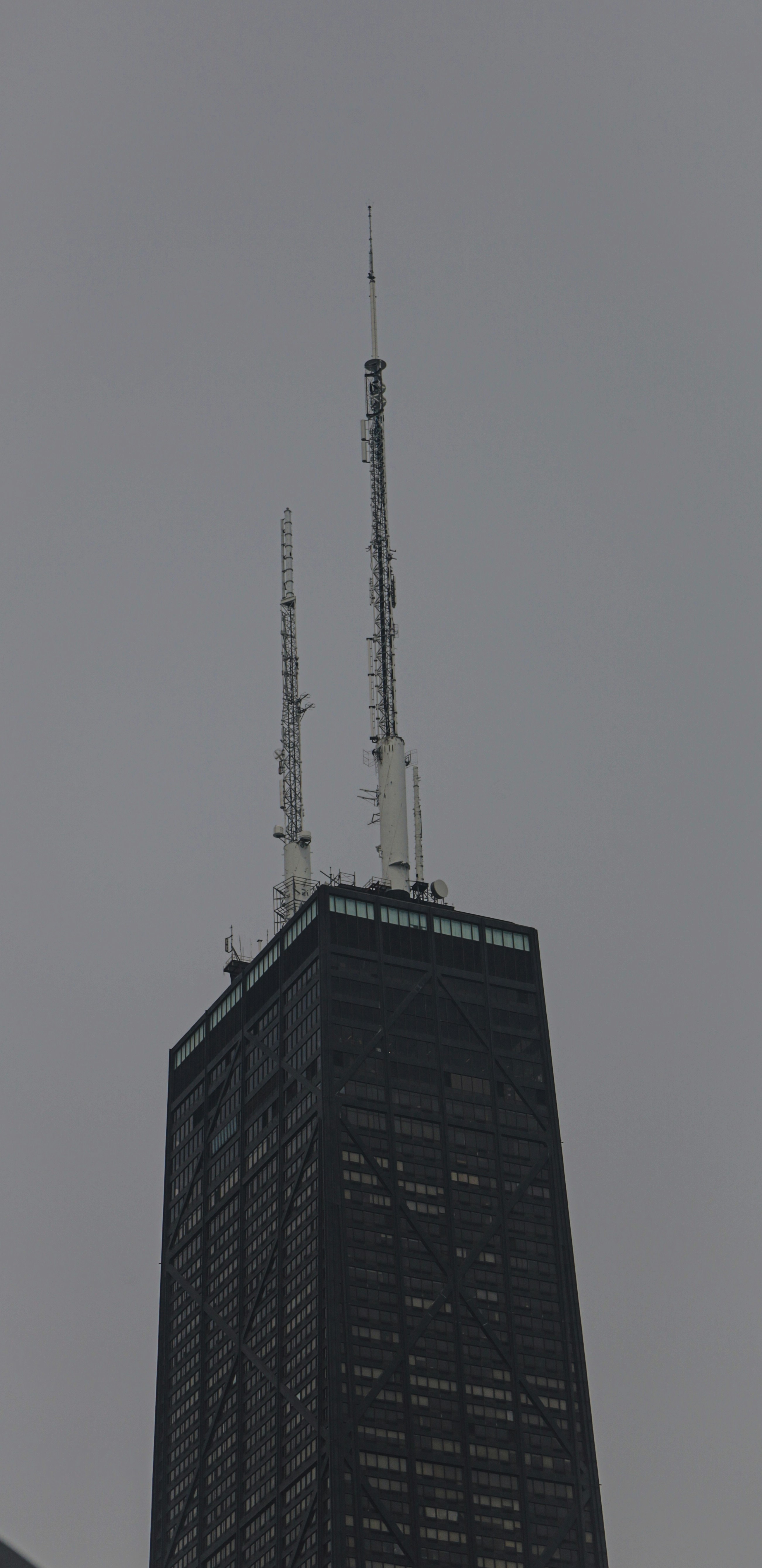 Telecommunication antennas atop a skyscraper against a cloudy sky, showcasing urban infrastructure and technology.