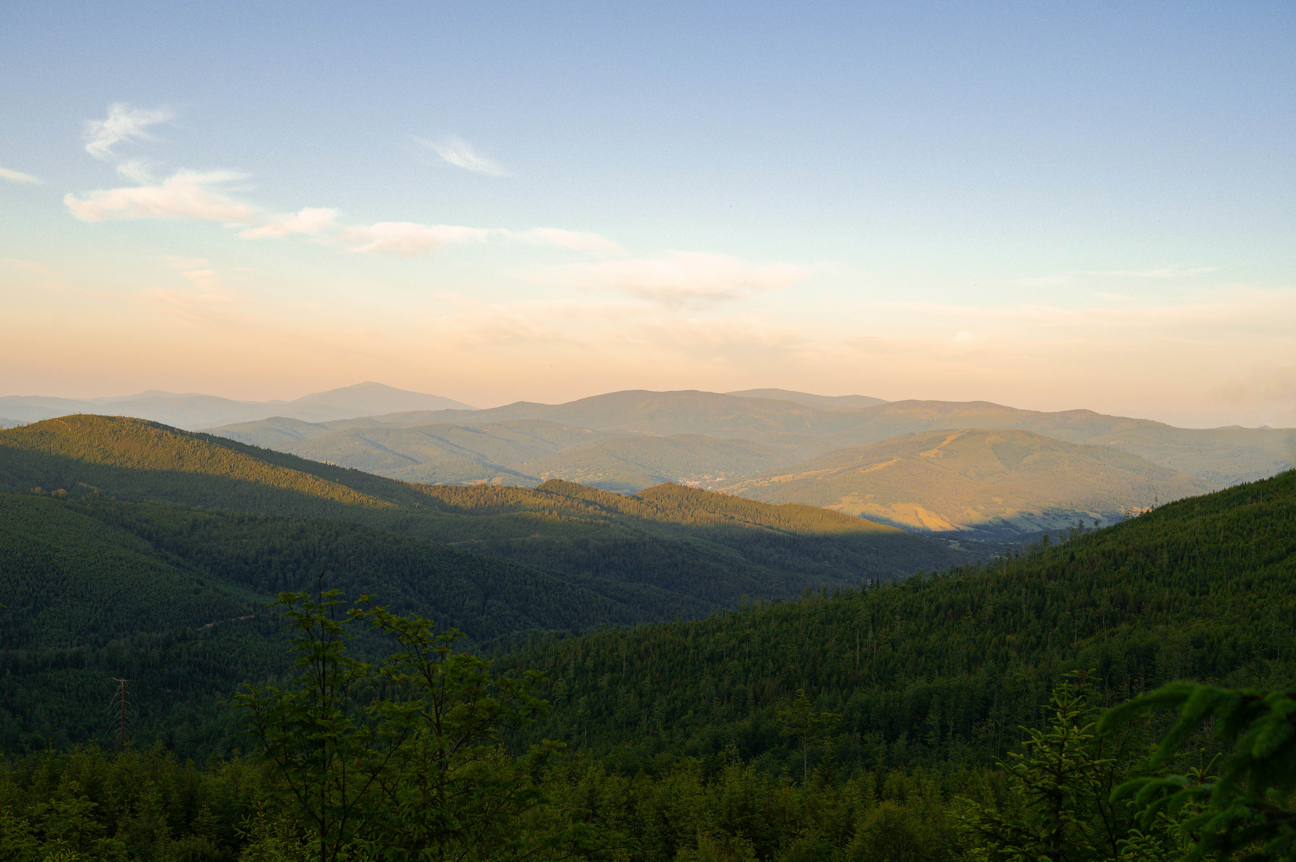 Vast expanse of rolling hills under a soft sky, showcasing layers of green and blue hues. The scene captures the serene beauty of nature's gradients.