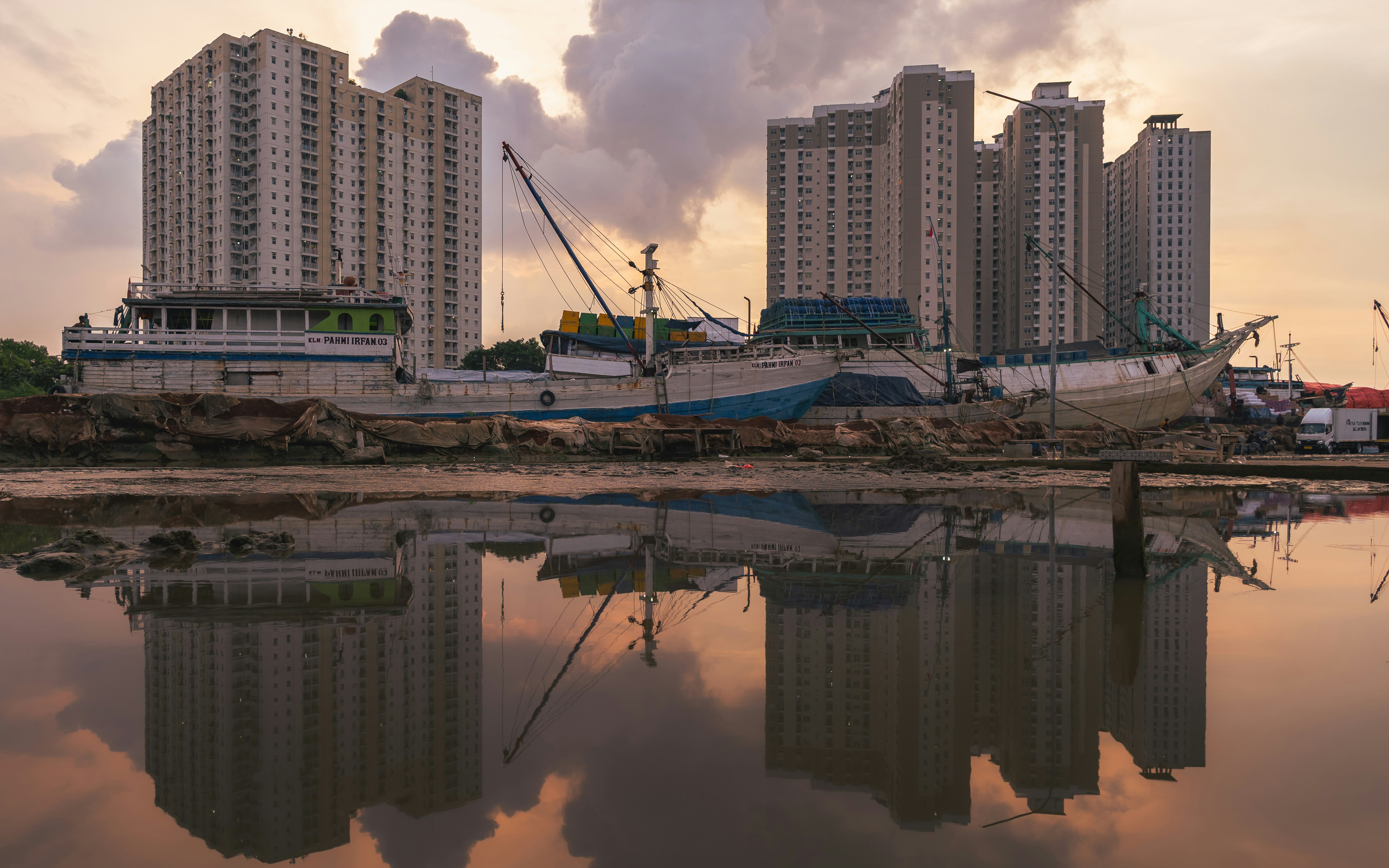 A boat is next to skyscrapers, reflecting in water.