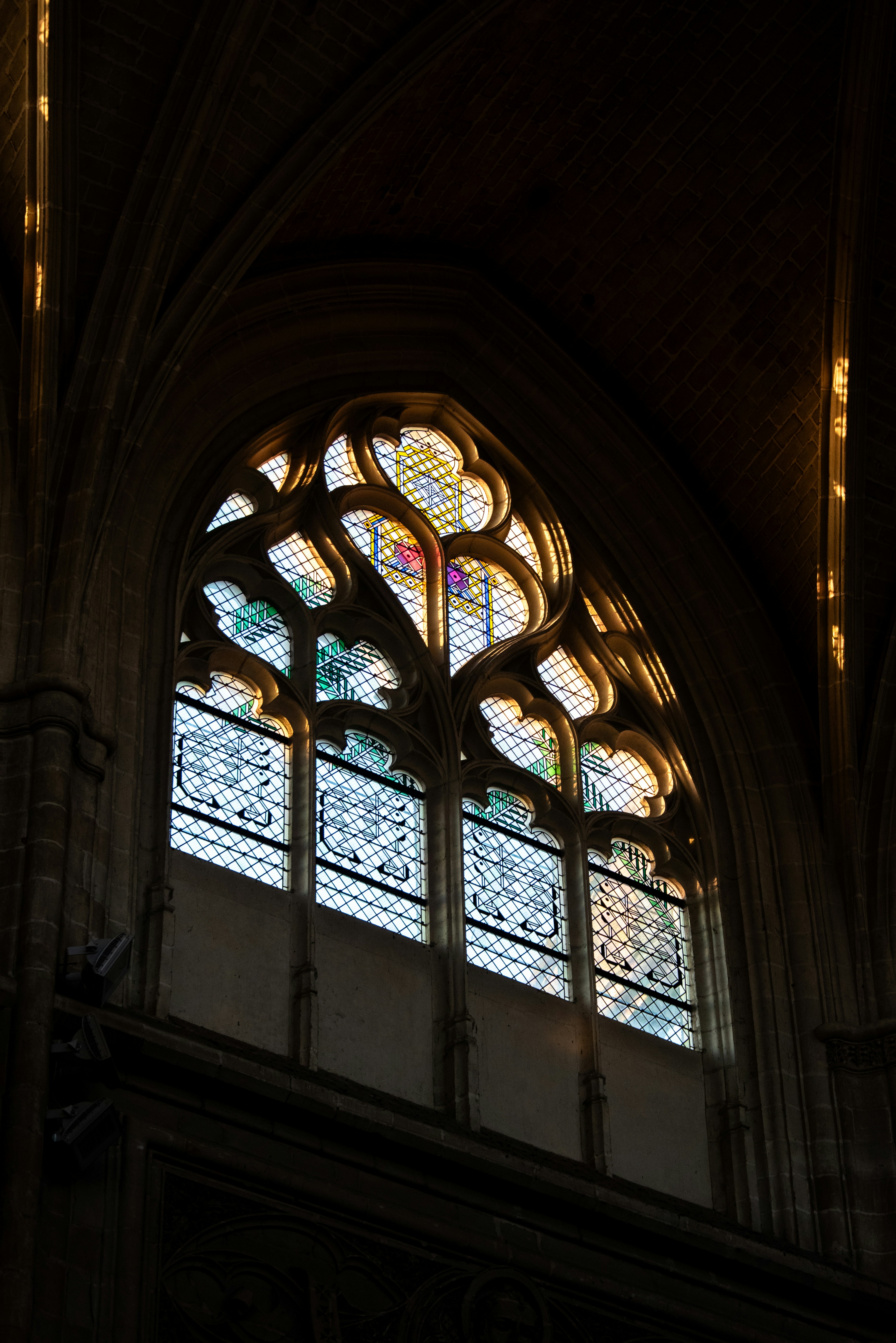 Intricate stained glass window casting colorful reflections in a historic building. The architectural details frame the vibrant glasswork.