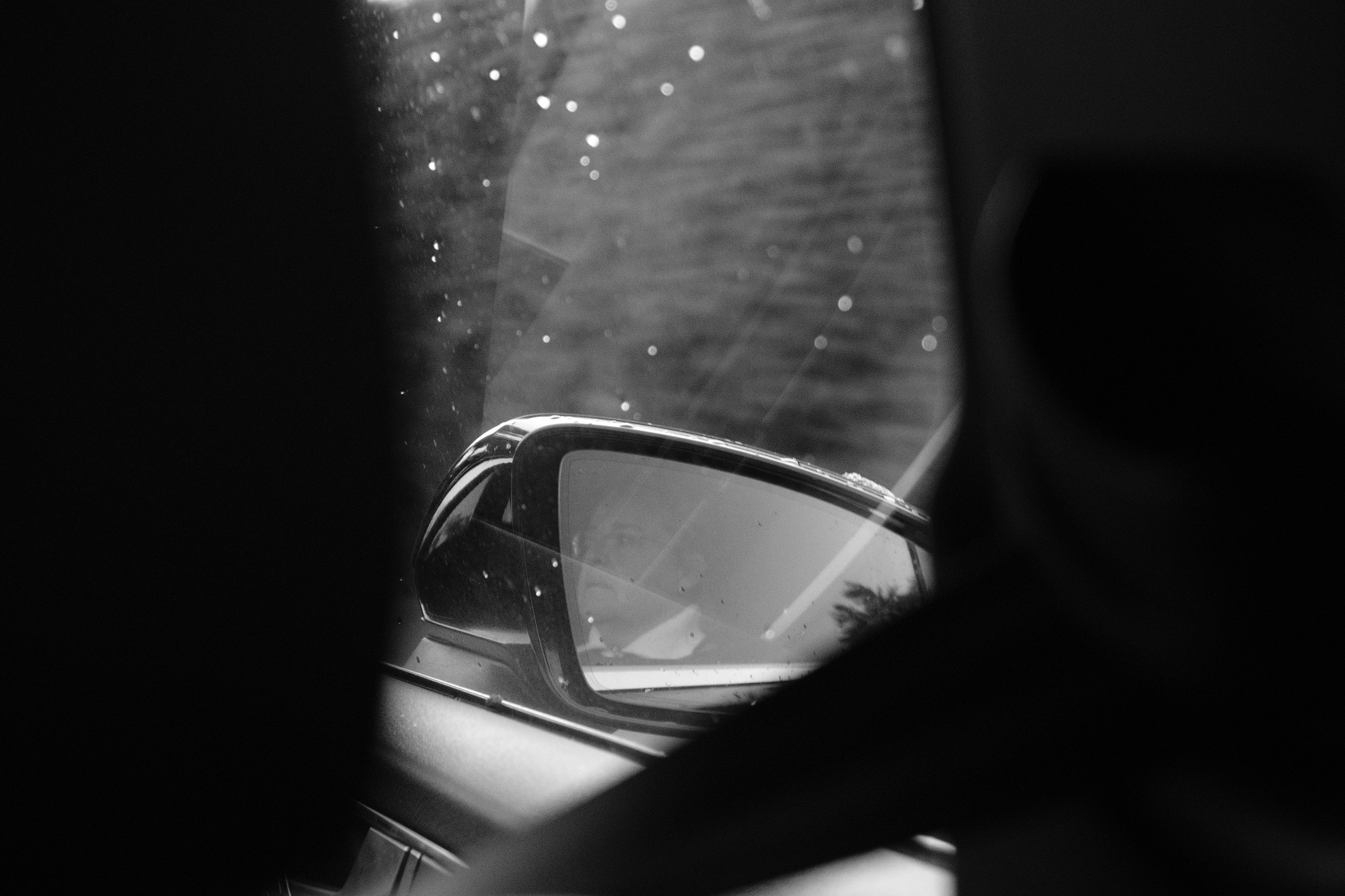 Side mirror reflecting the blurred landscape, framed by the interior of a vehicle. The scene captures the essence of travel and fleeting moments.