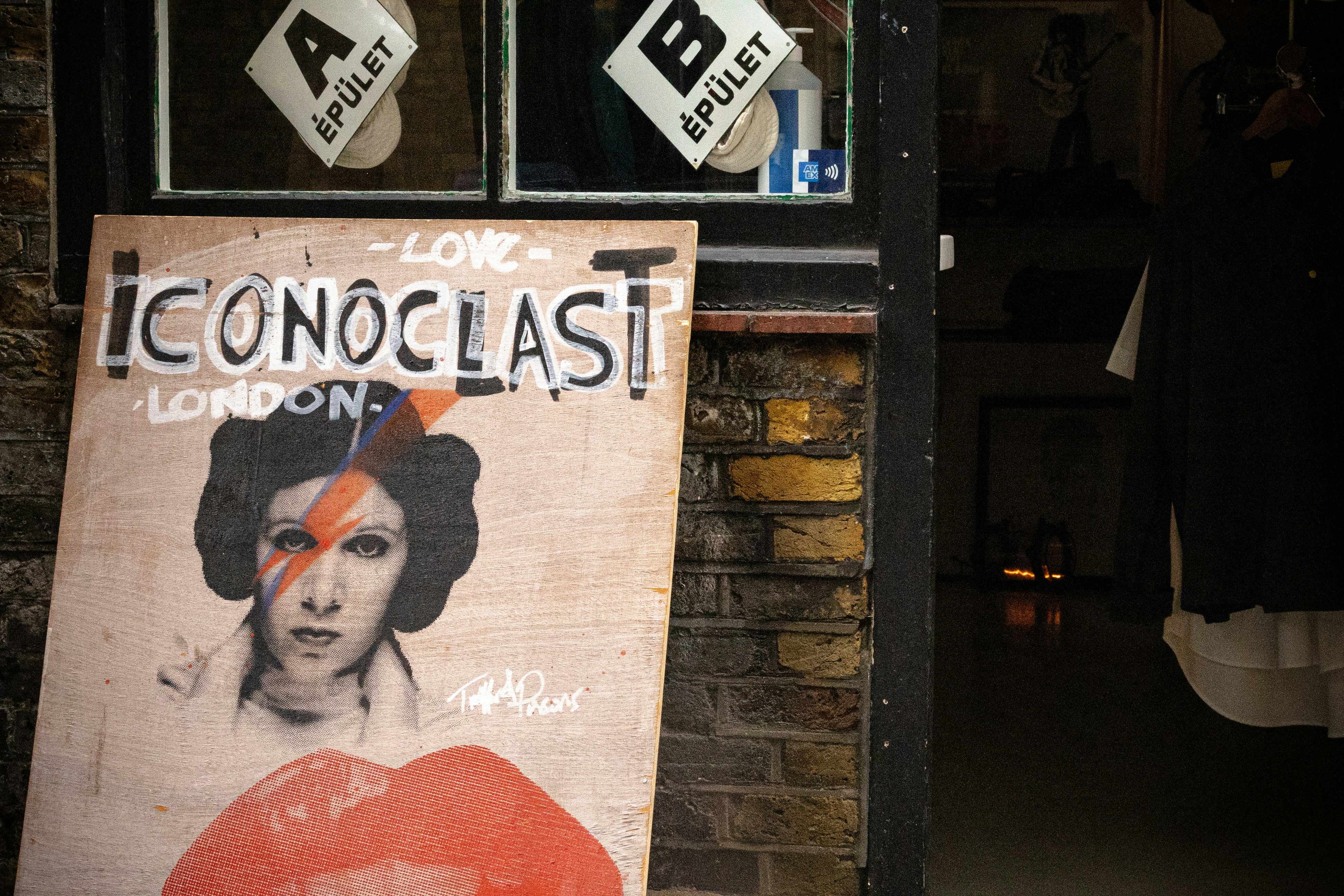 A vibrant street art piece featuring a stylized portrait with bold text, set against a rustic brick wall. The artwork reflects a blend of cultural commentary and urban aesthetics.