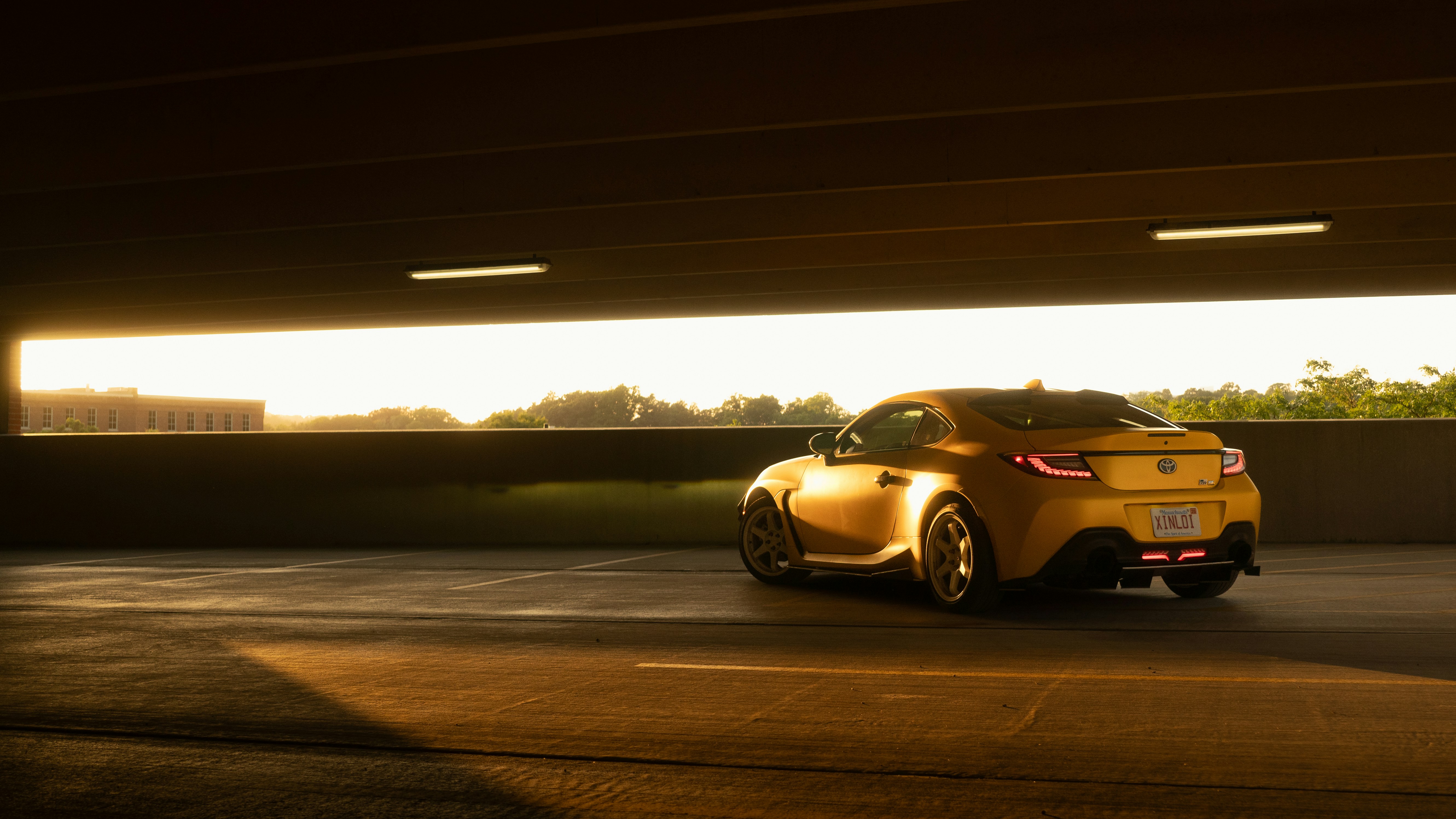 A sleek yellow sports car parked in a dimly lit garage, illuminated by golden sunlight streaming through an opening. The scene captures the interplay of light and shadow.