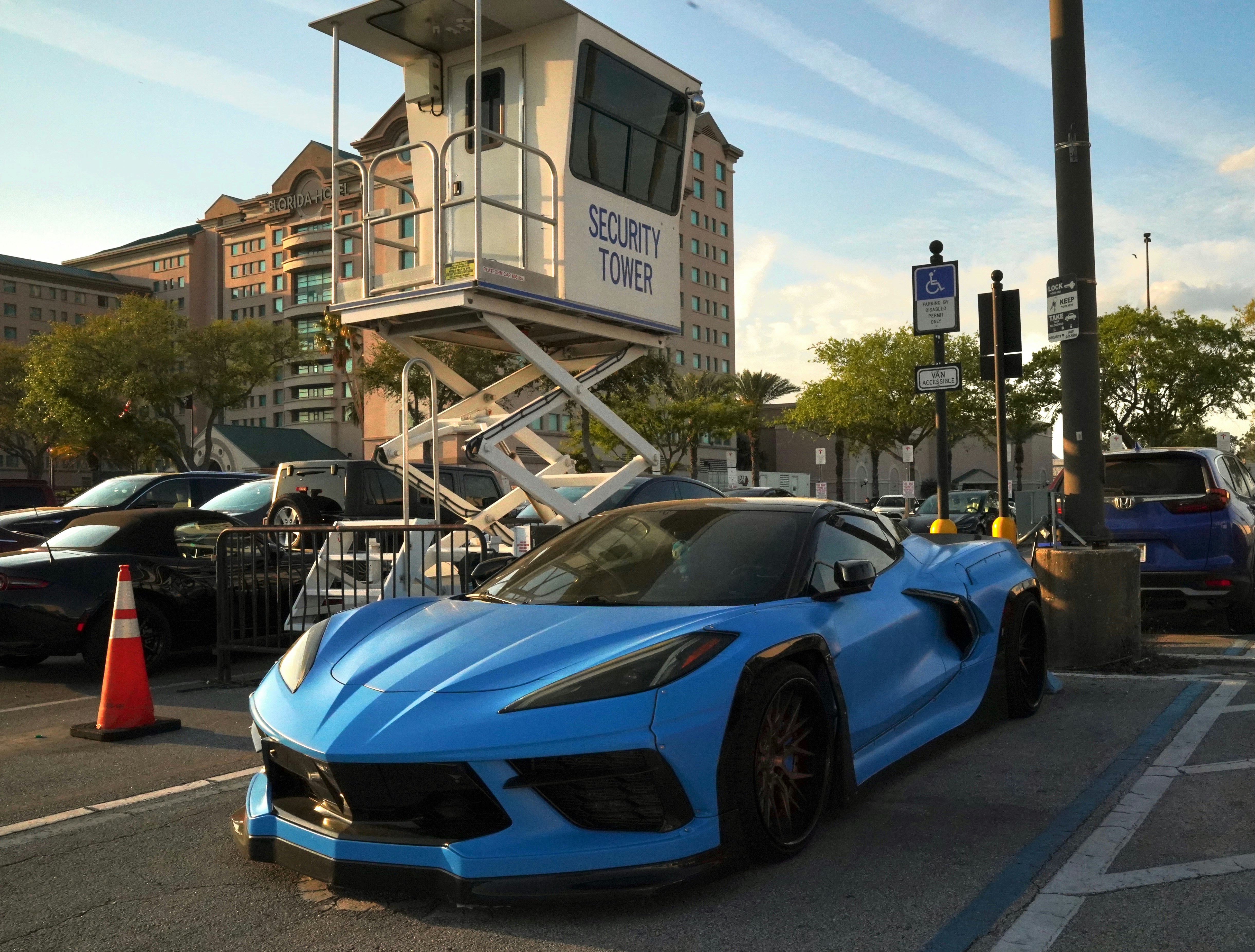 Azure Velocity in a Sunlit Lot: Corvette Beneath a Guarded Tower