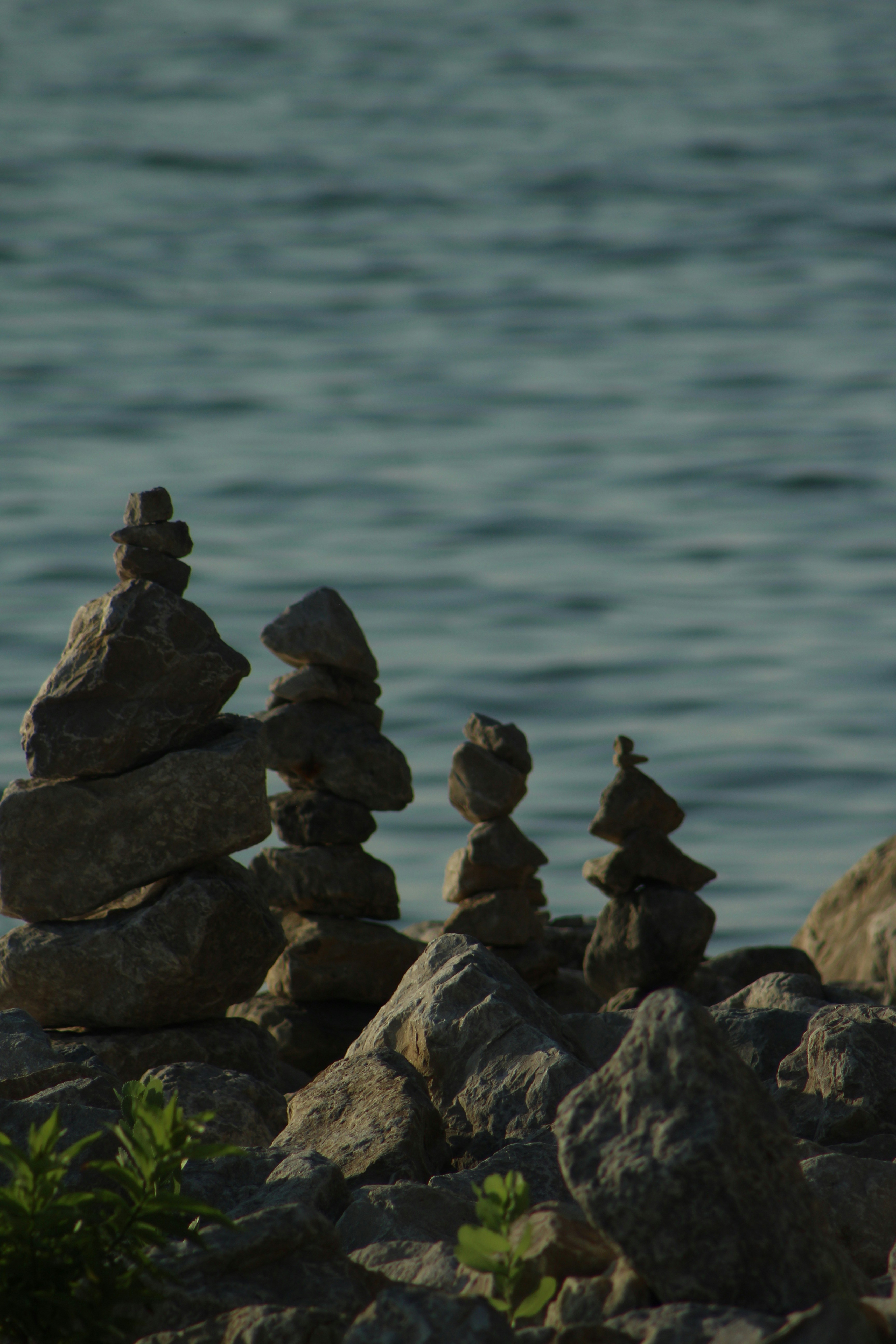 Stone cairns stand on a rocky shore by the water.