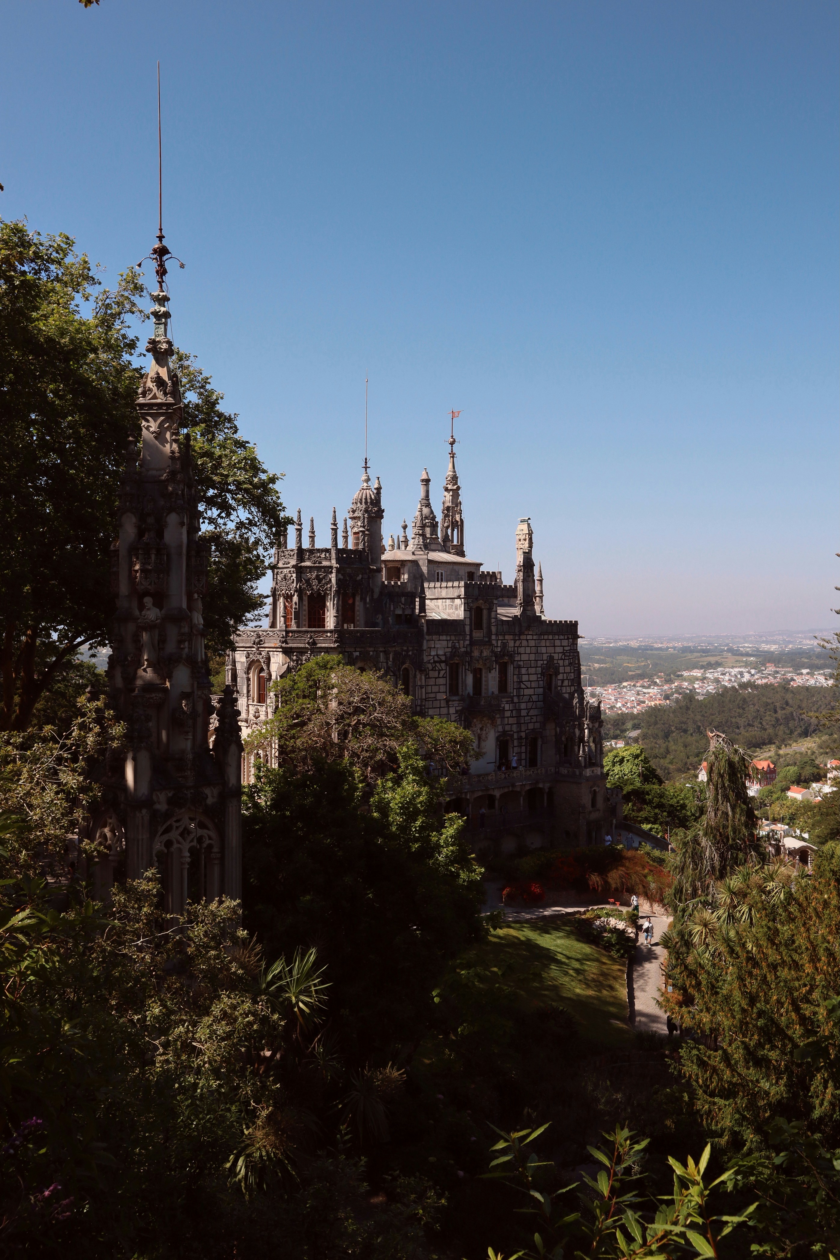 Intricately designed manor nestled among lush greenery, showcasing Gothic architectural elements against a clear blue sky.