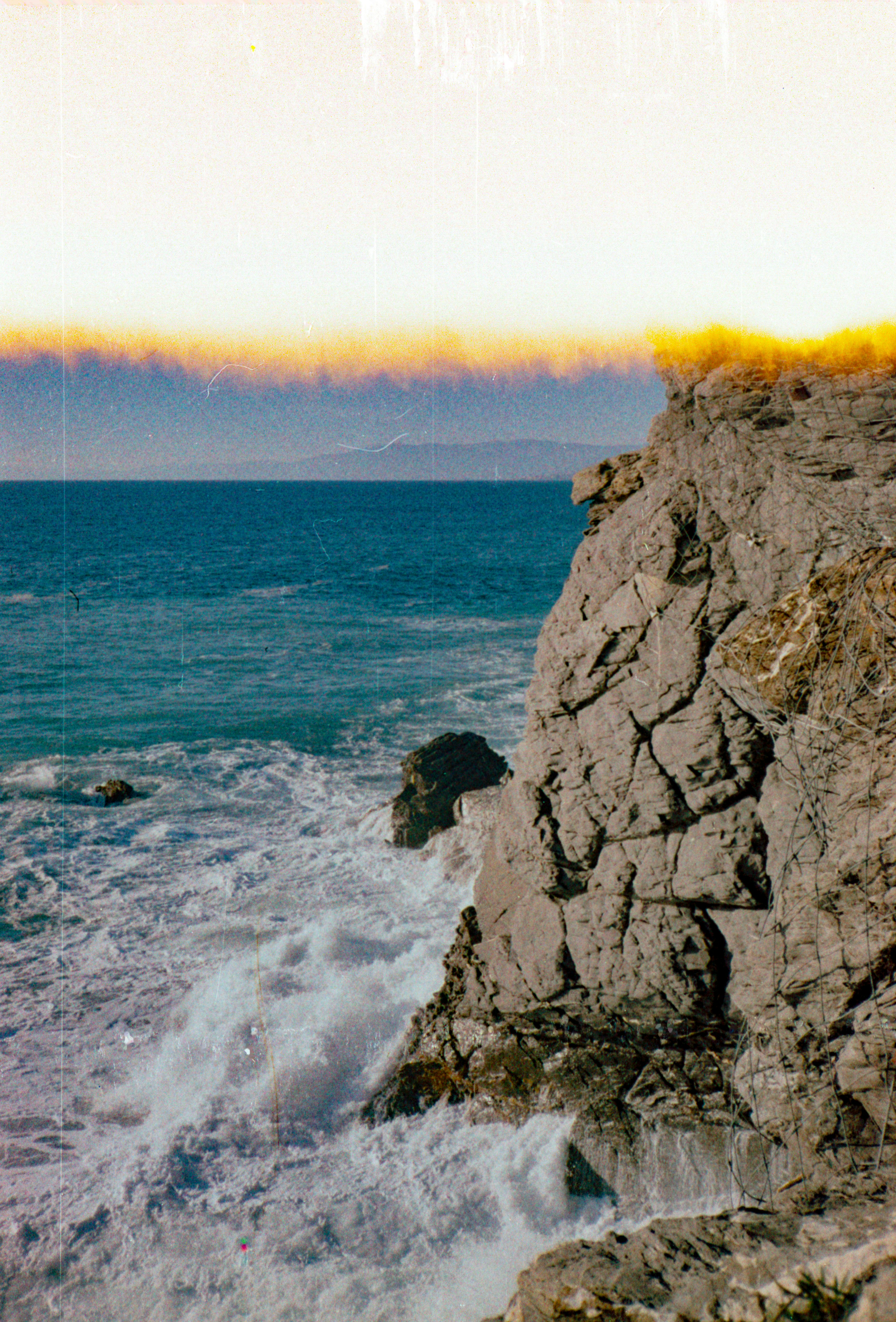 Waves crash against a rocky cliff by the sea.