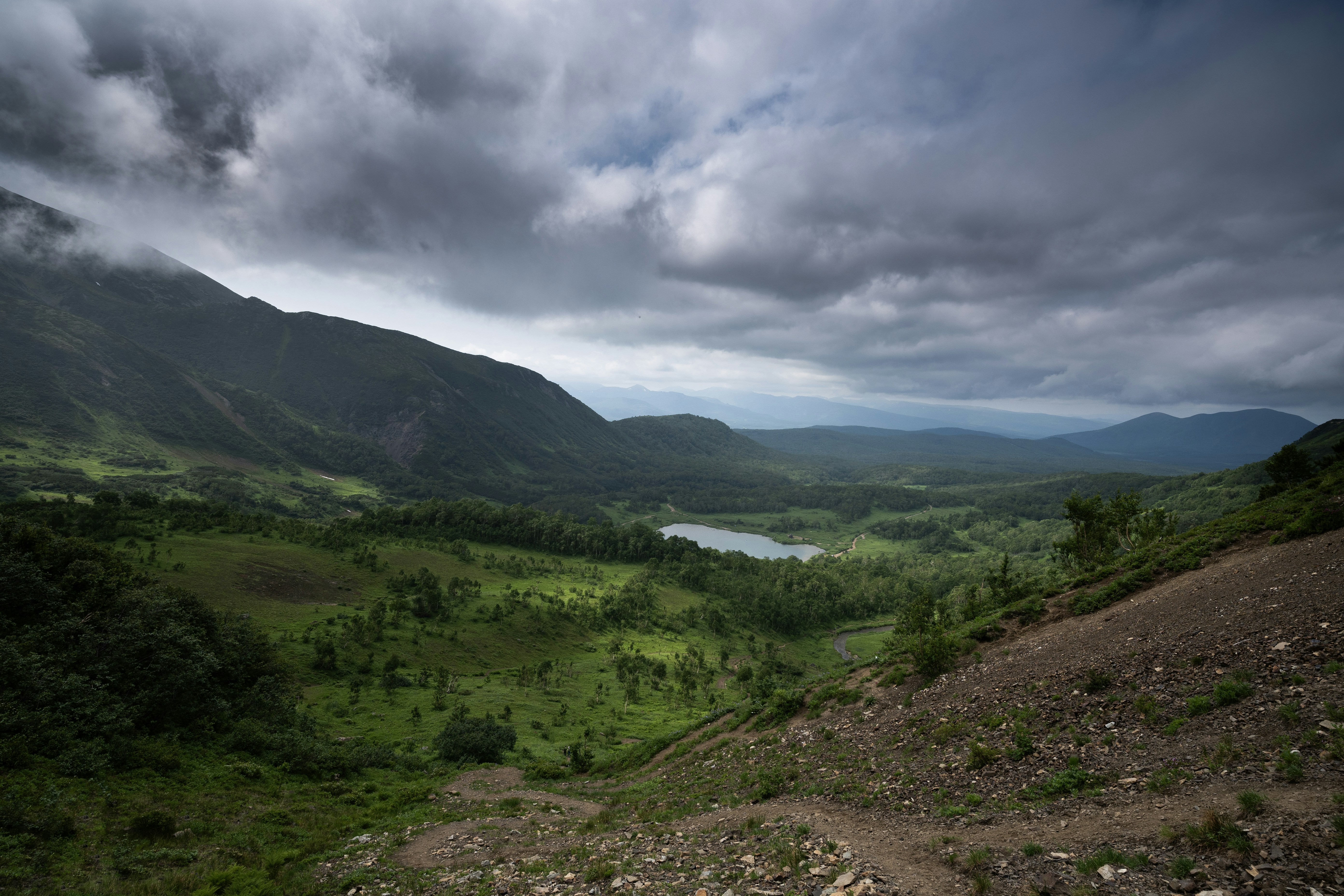 Vachkazhets mountain range (Kamchatka - 53,081395, 157,929445) | Dramatic, cloudy landscape with green valley below.