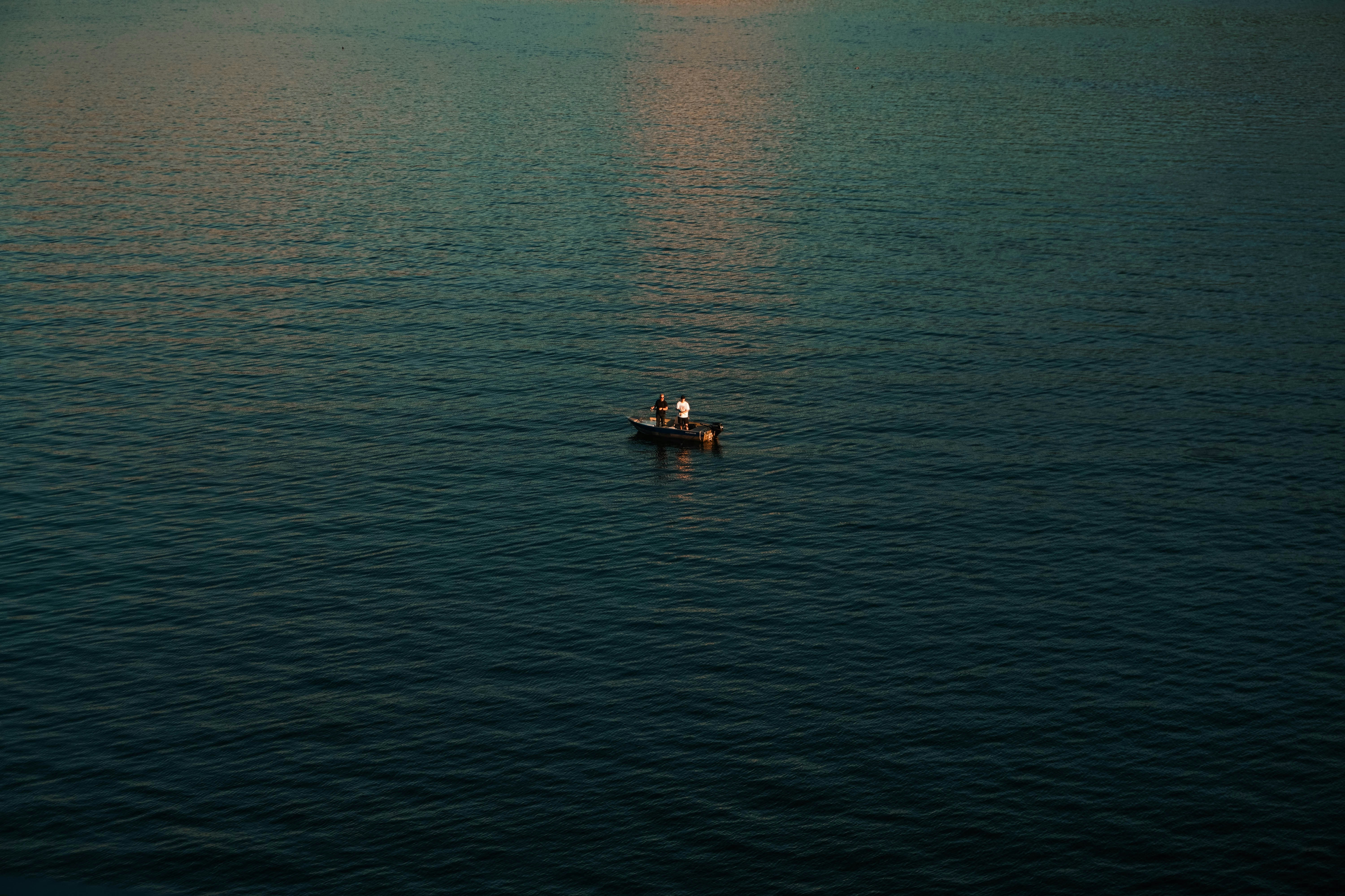 A small boat gently gliding across a calm sea, surrounded by tranquil water reflecting soft hues of dusk.