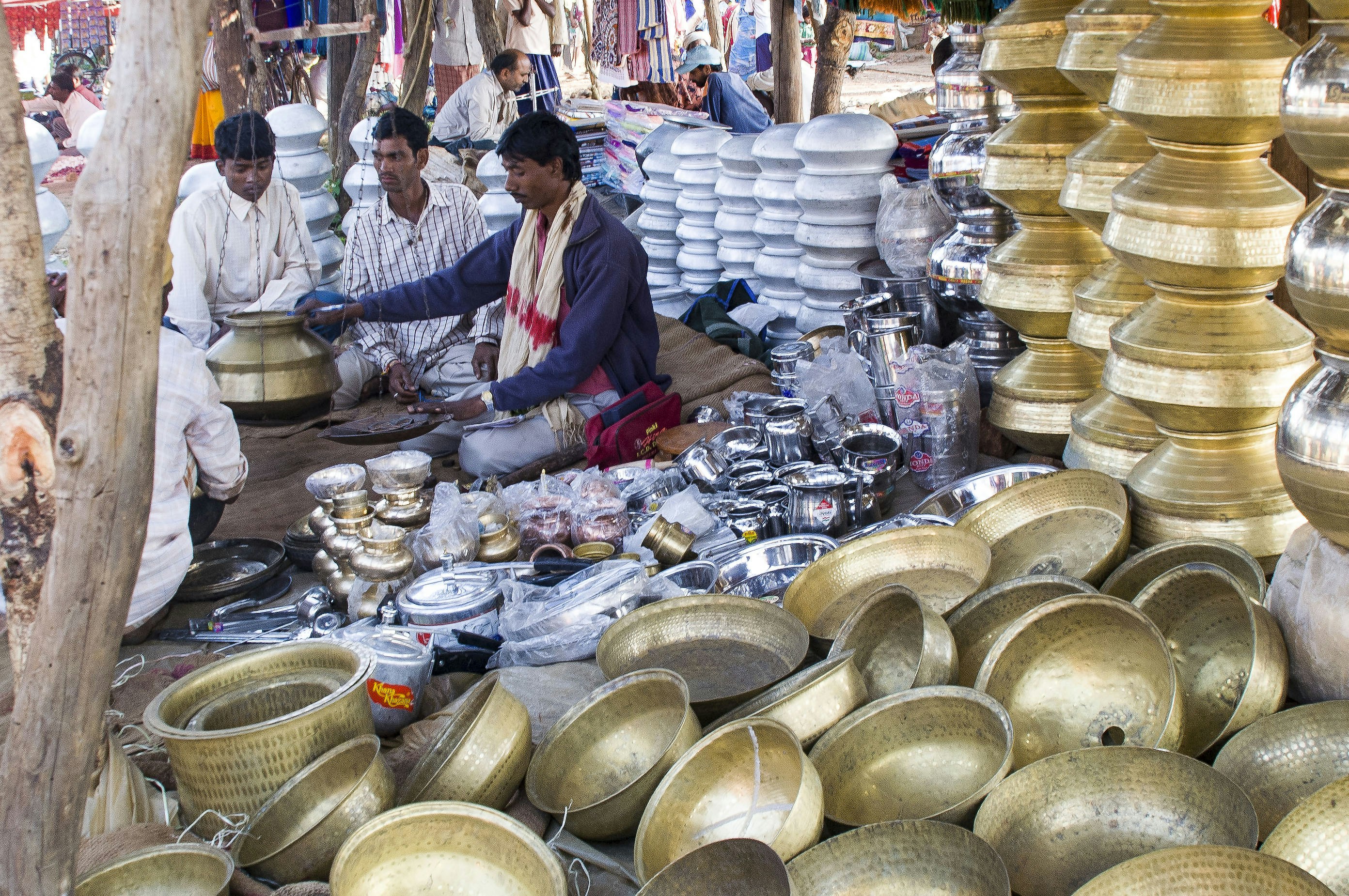 Artisans engaged in crafting and selling metalware at a bustling market, surrounded by an array of shiny bowls and utensils.