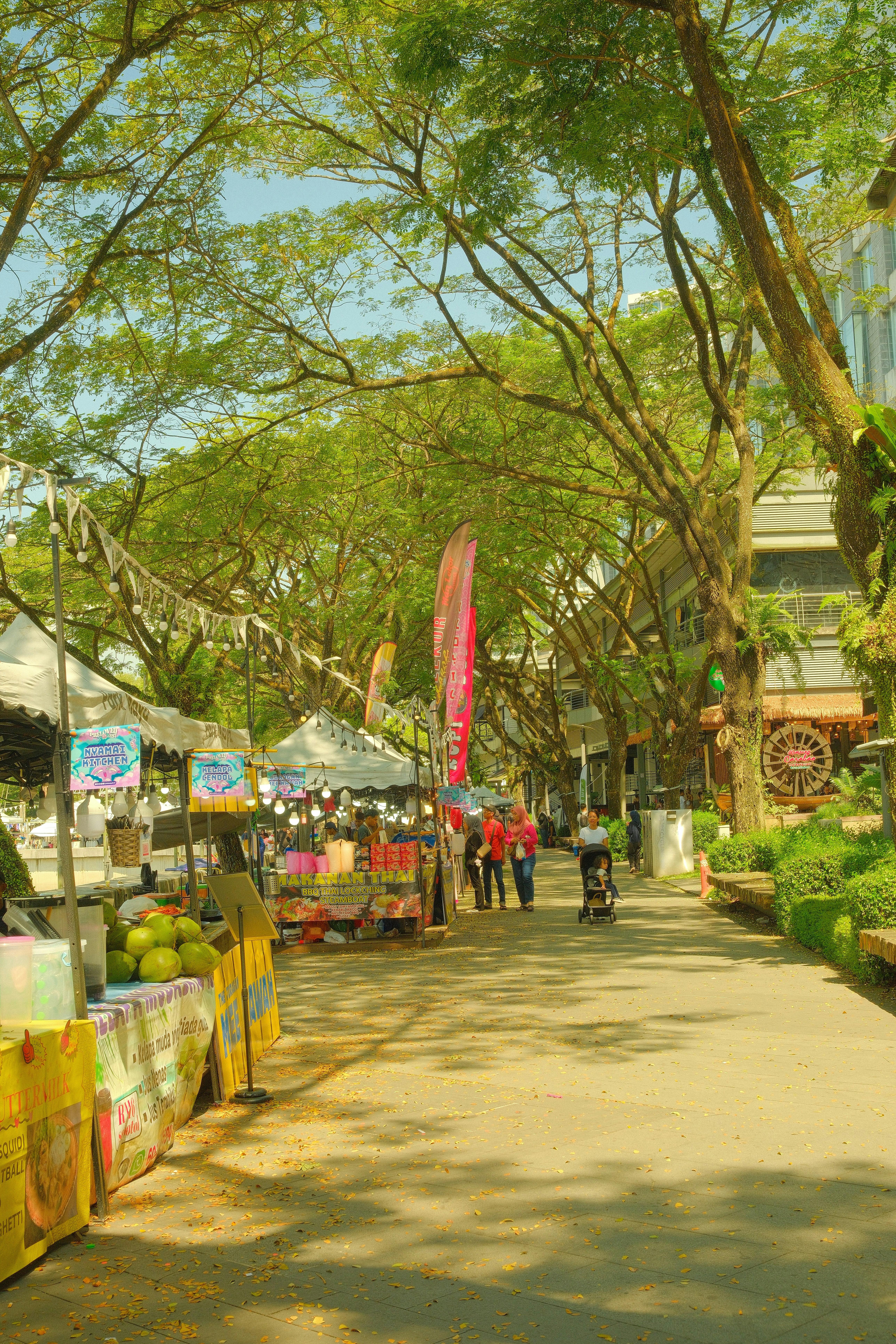 Preloved Fest at Marina Walk, Puteri Harbour. | Shaded walkway with vendors and lush trees.