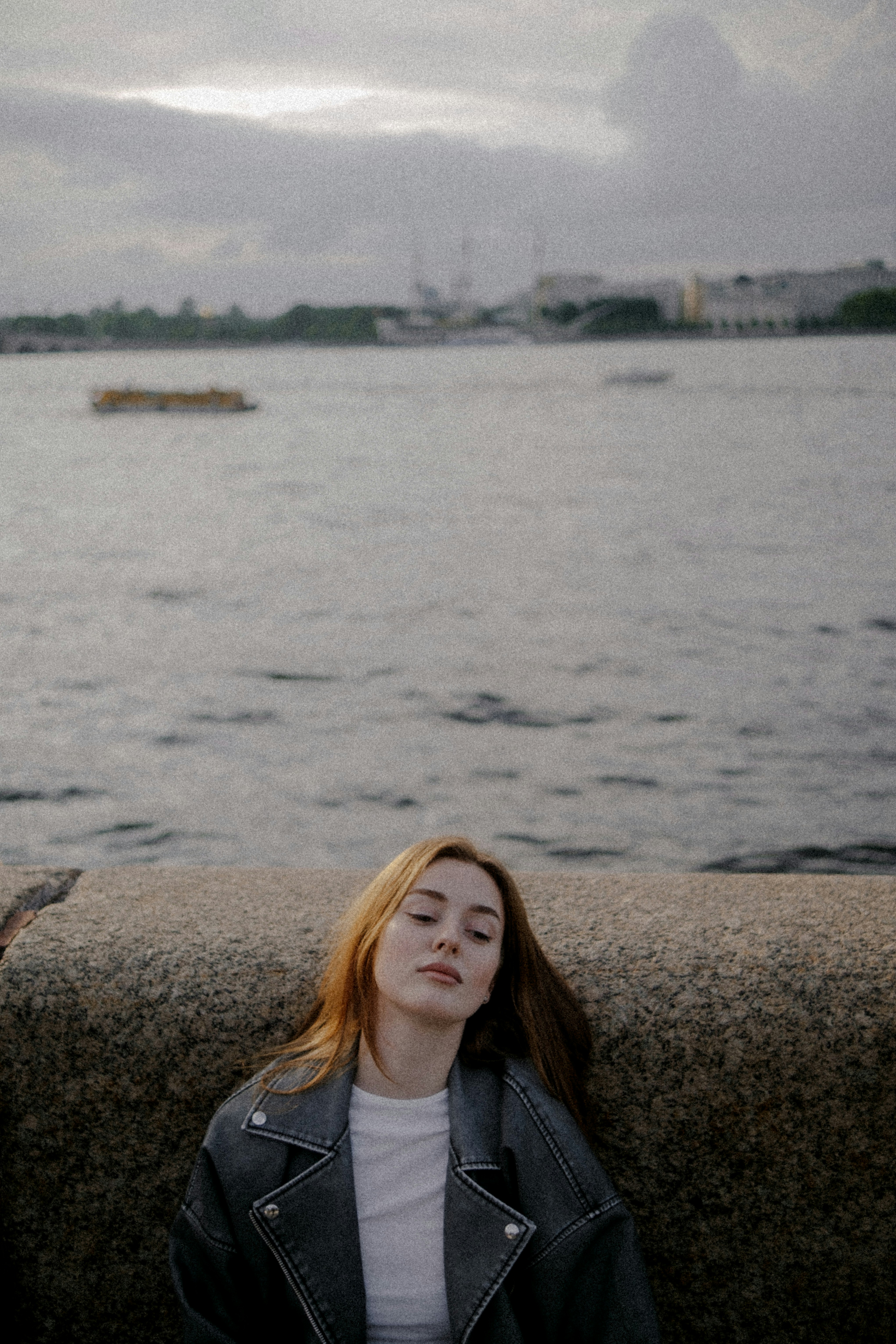 Woman leans against wall by a body of water.