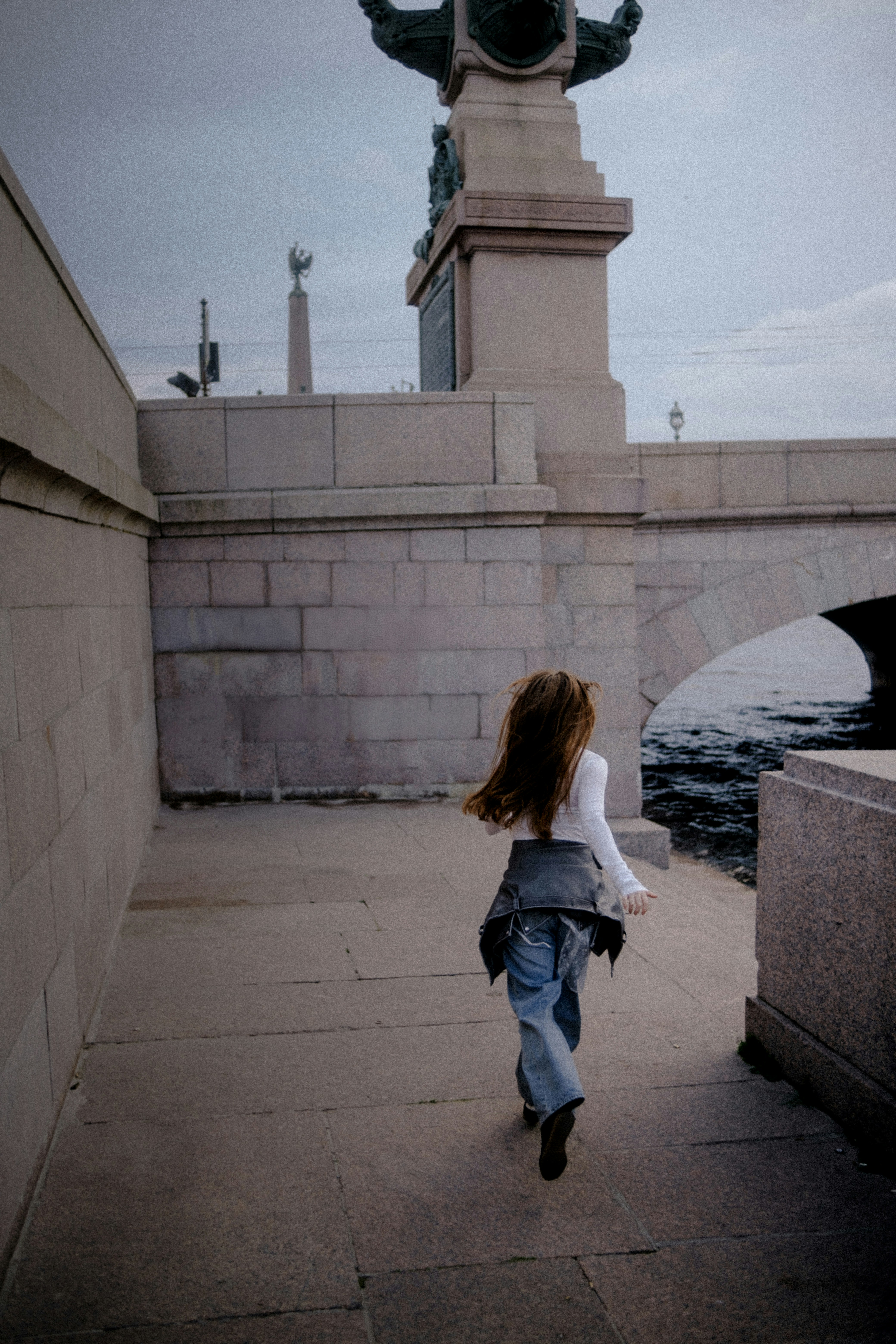 Under the Monument Arc: a girl sprints along the stone riverfront