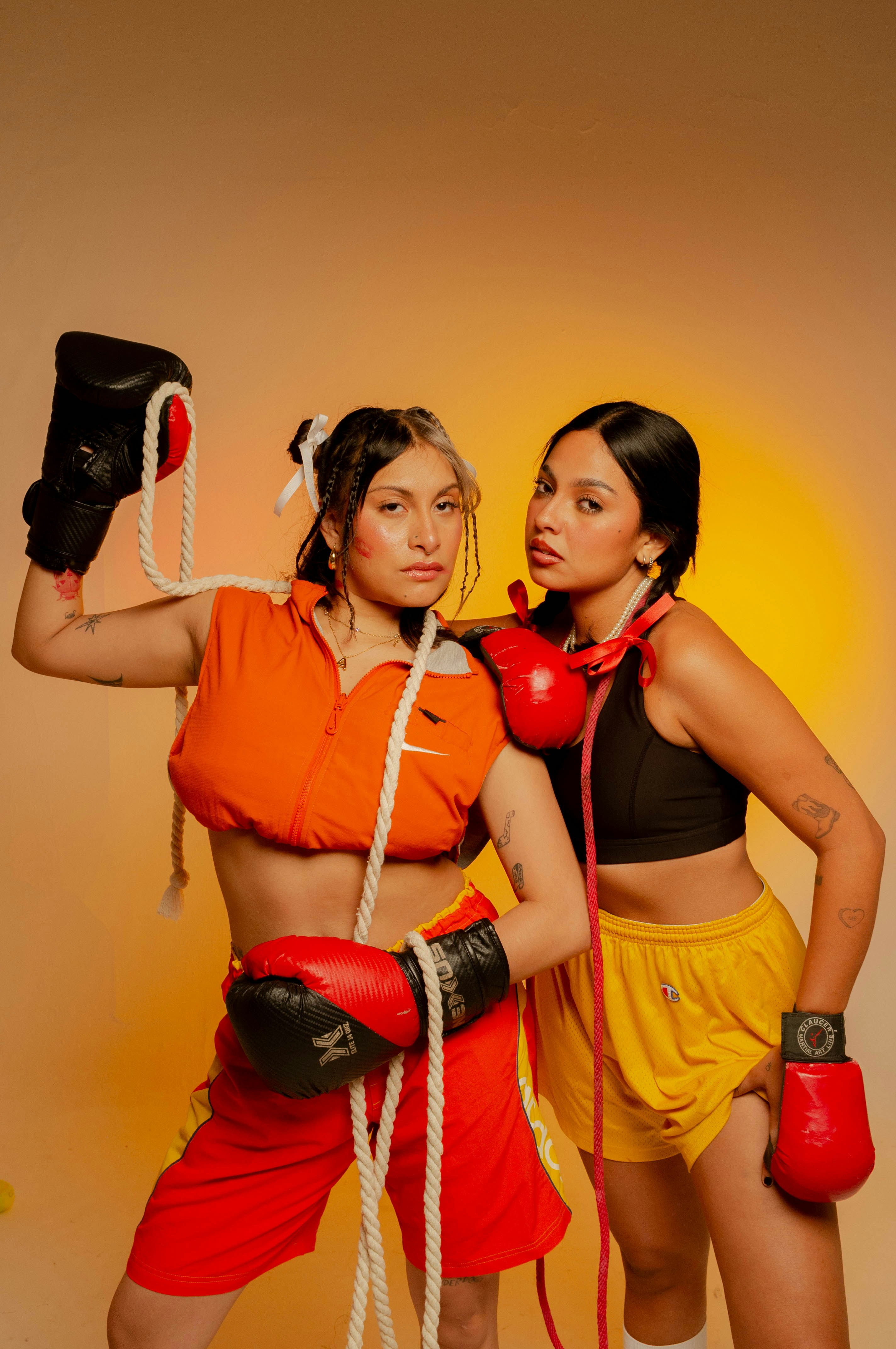 Two women pose with boxing gloves and rope.