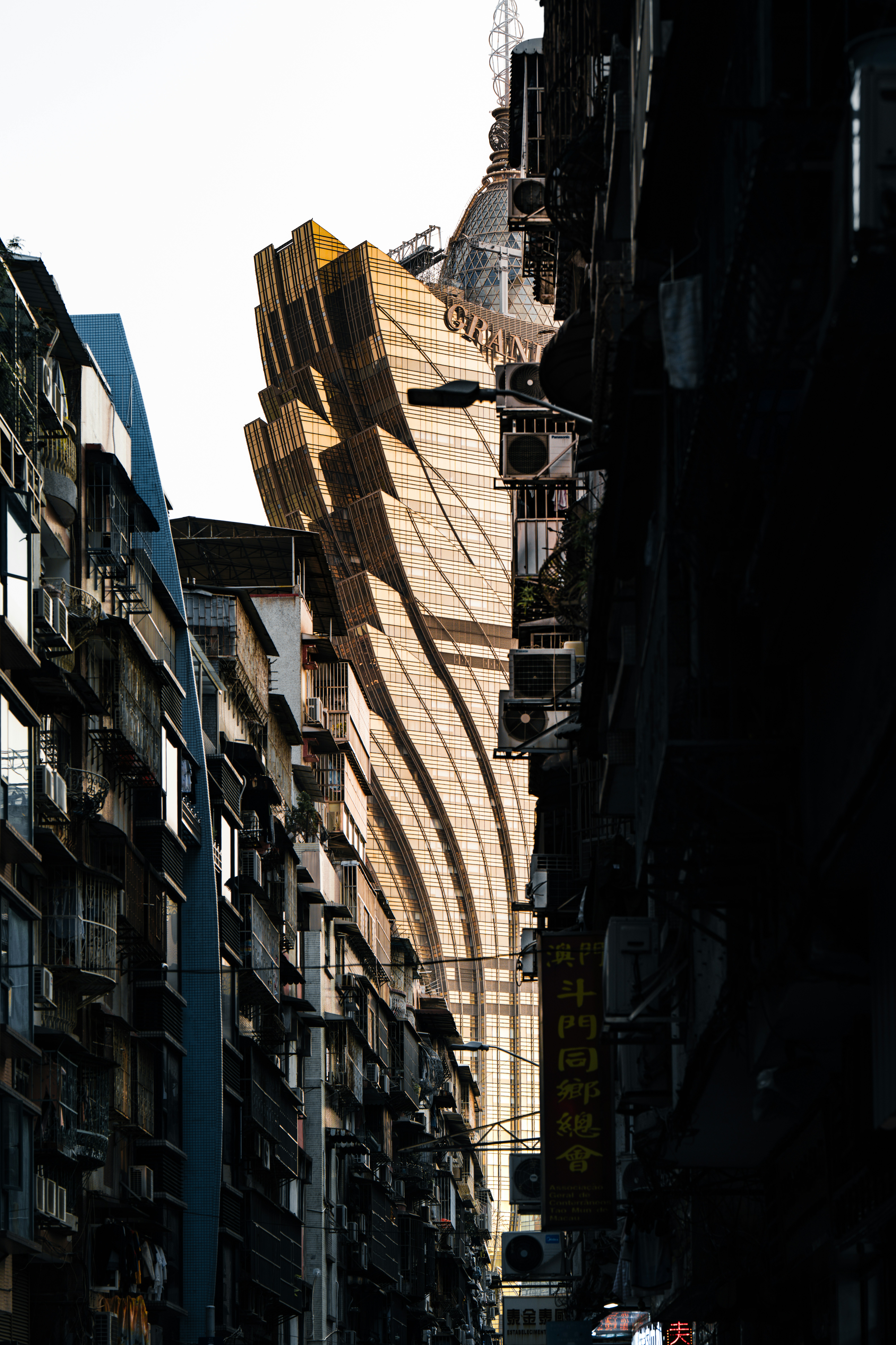 A modern skyscraper with a striking golden facade rises above narrow city streets lined with older buildings. The contrast highlights the blend of architecture in an urban landscape.