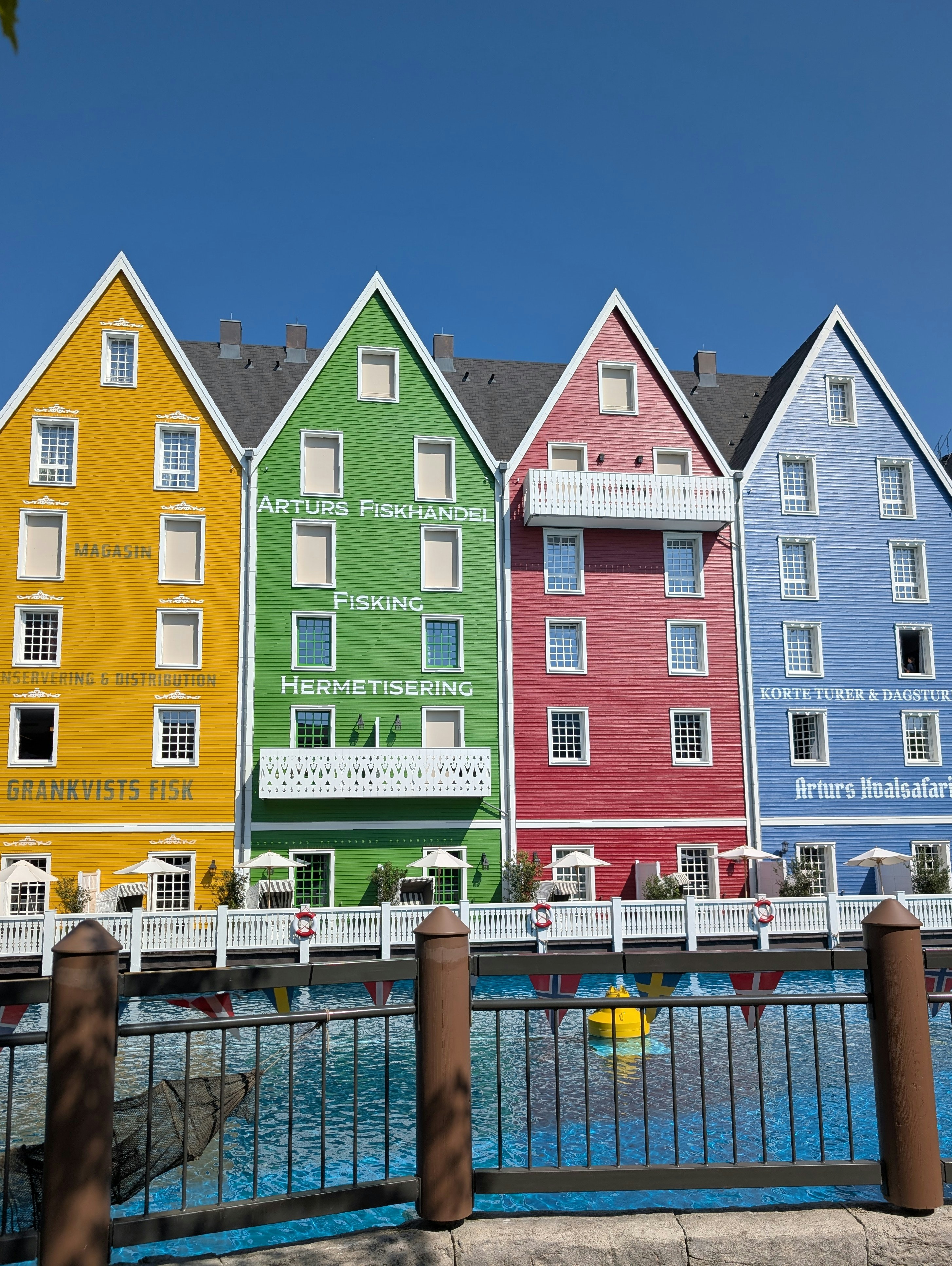 Vibrant, multi-colored buildings lining a serene waterfront, showcasing unique architectural styles and inviting signage. A picturesque scene reflecting local culture and commerce.