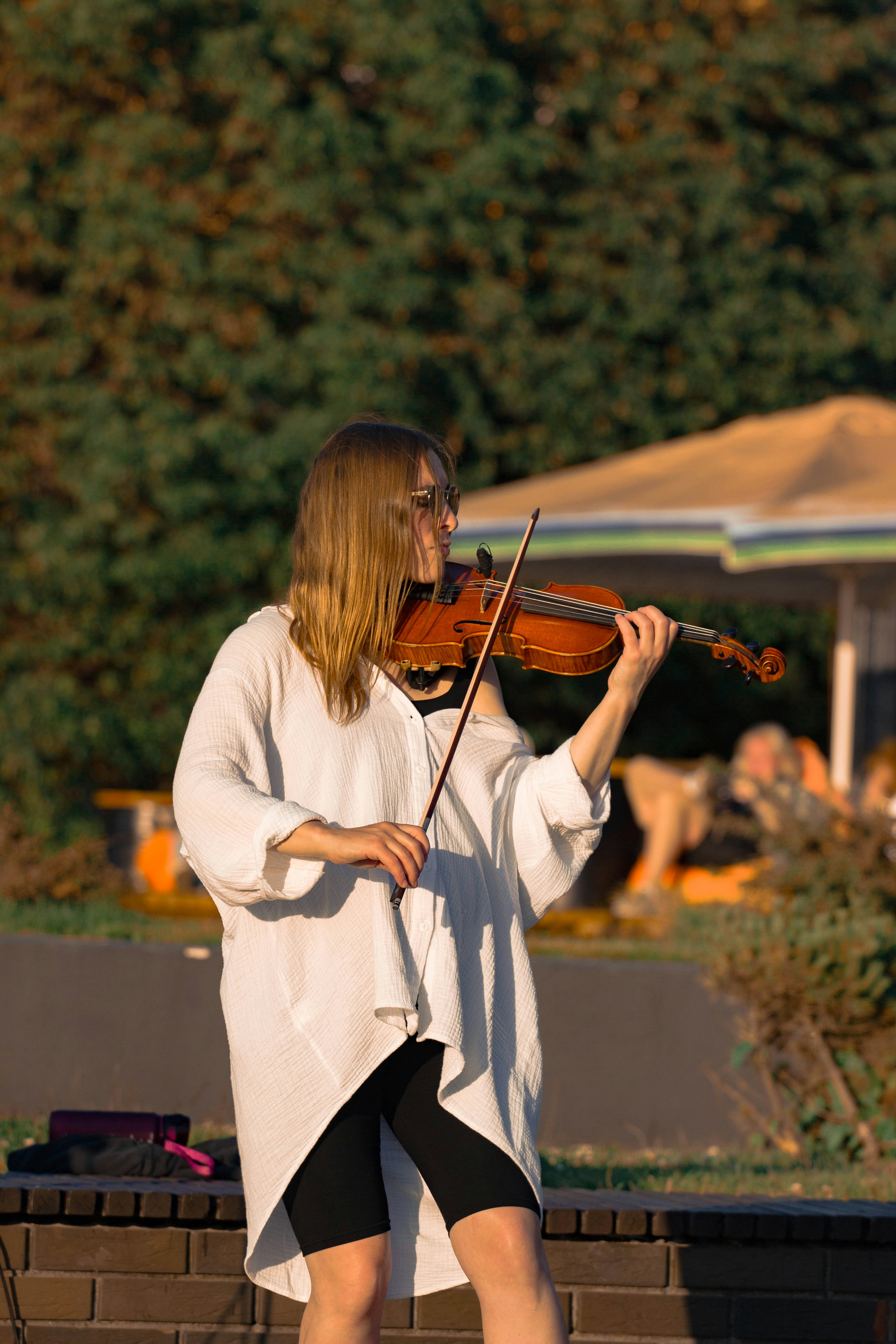 Young woman playing violin in golden sunset light, Taken during performance in outdoor venue. Perfect for art, street culture theme.