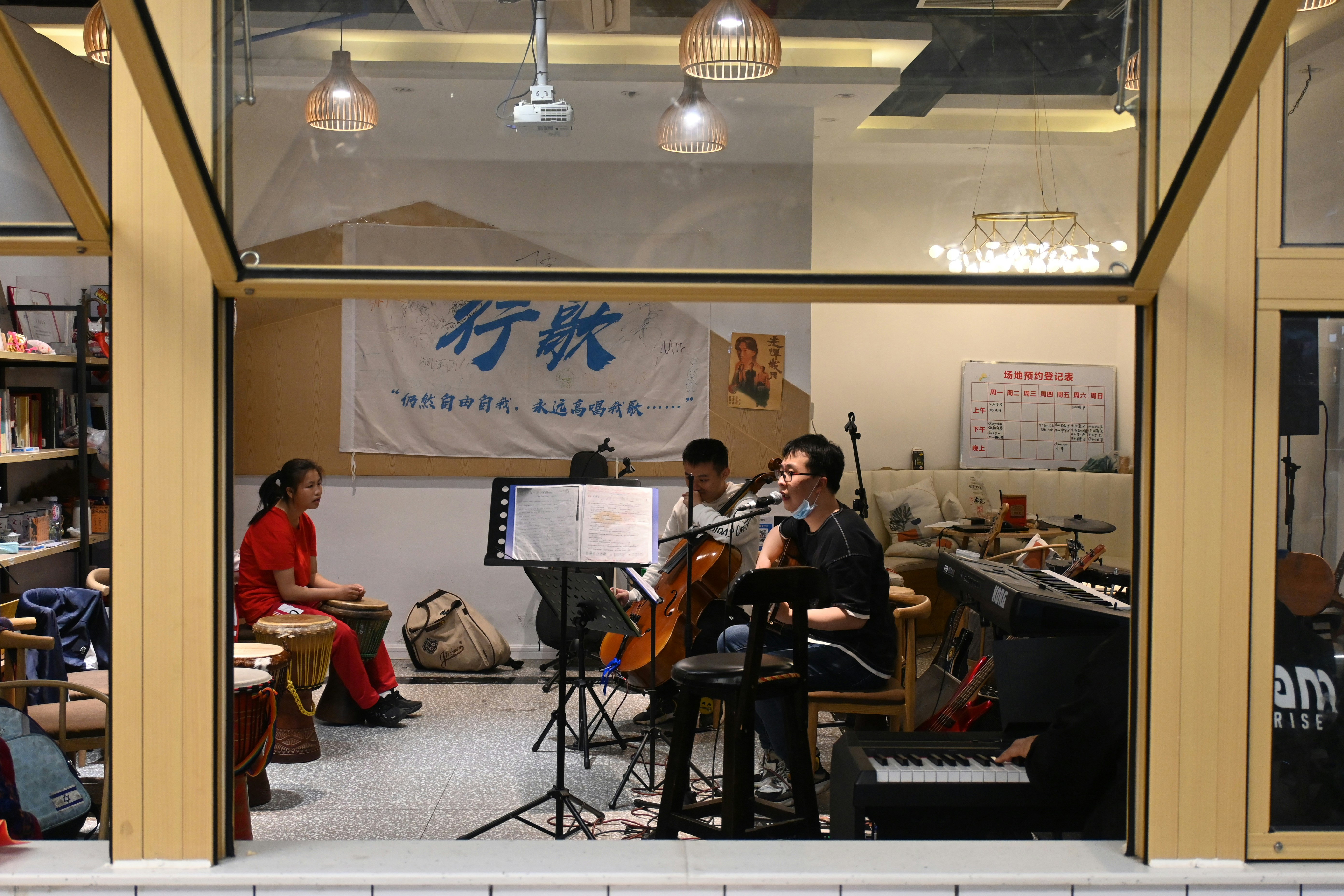 Musicians performing in a cozy café setting, surrounded by instruments and a warm atmosphere. A banner with Chinese characters hangs in the background.