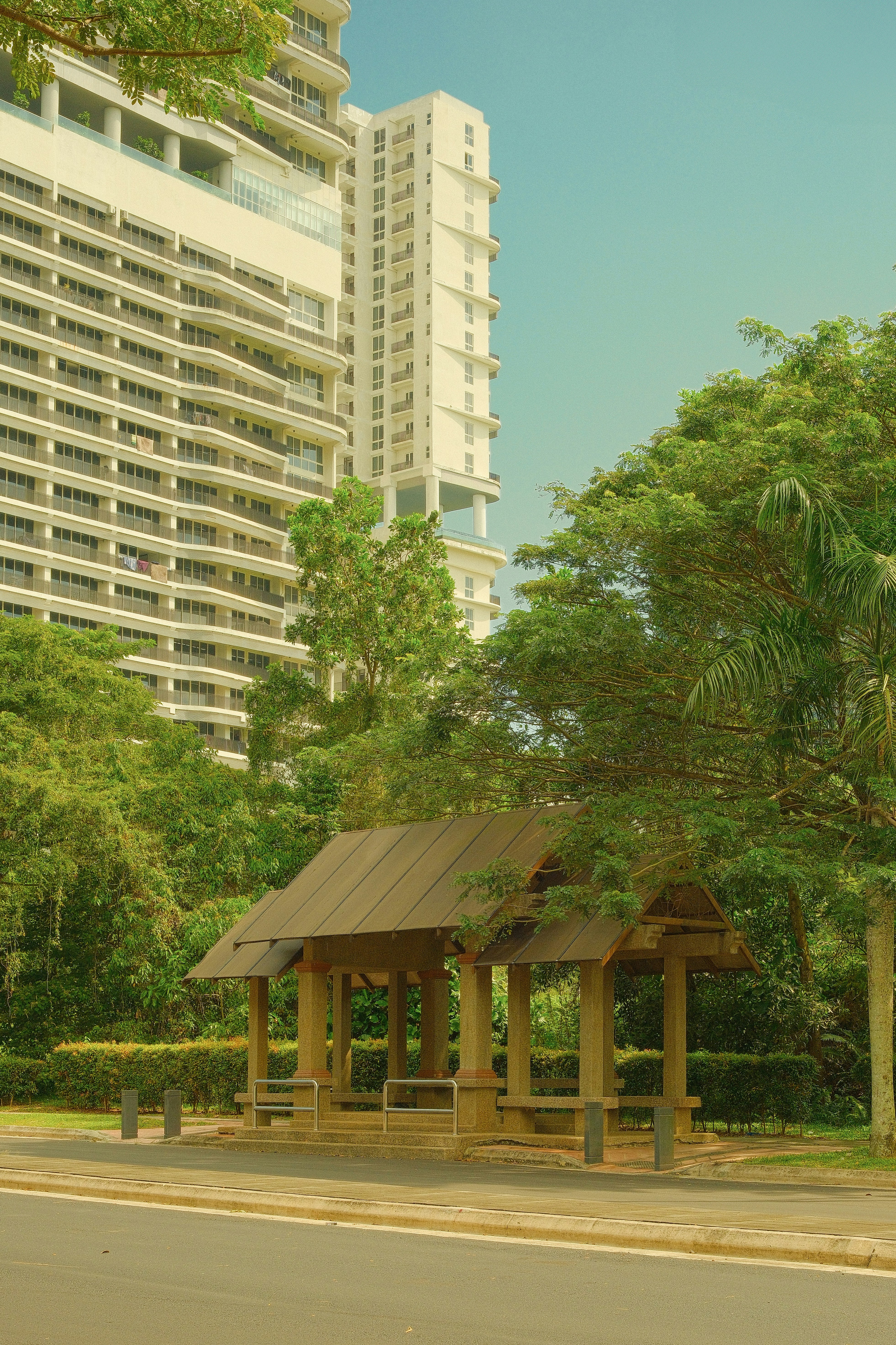 A rustic gazebo surrounded by lush greenery and towering residential buildings, highlighting the contrast between nature and urban architecture.