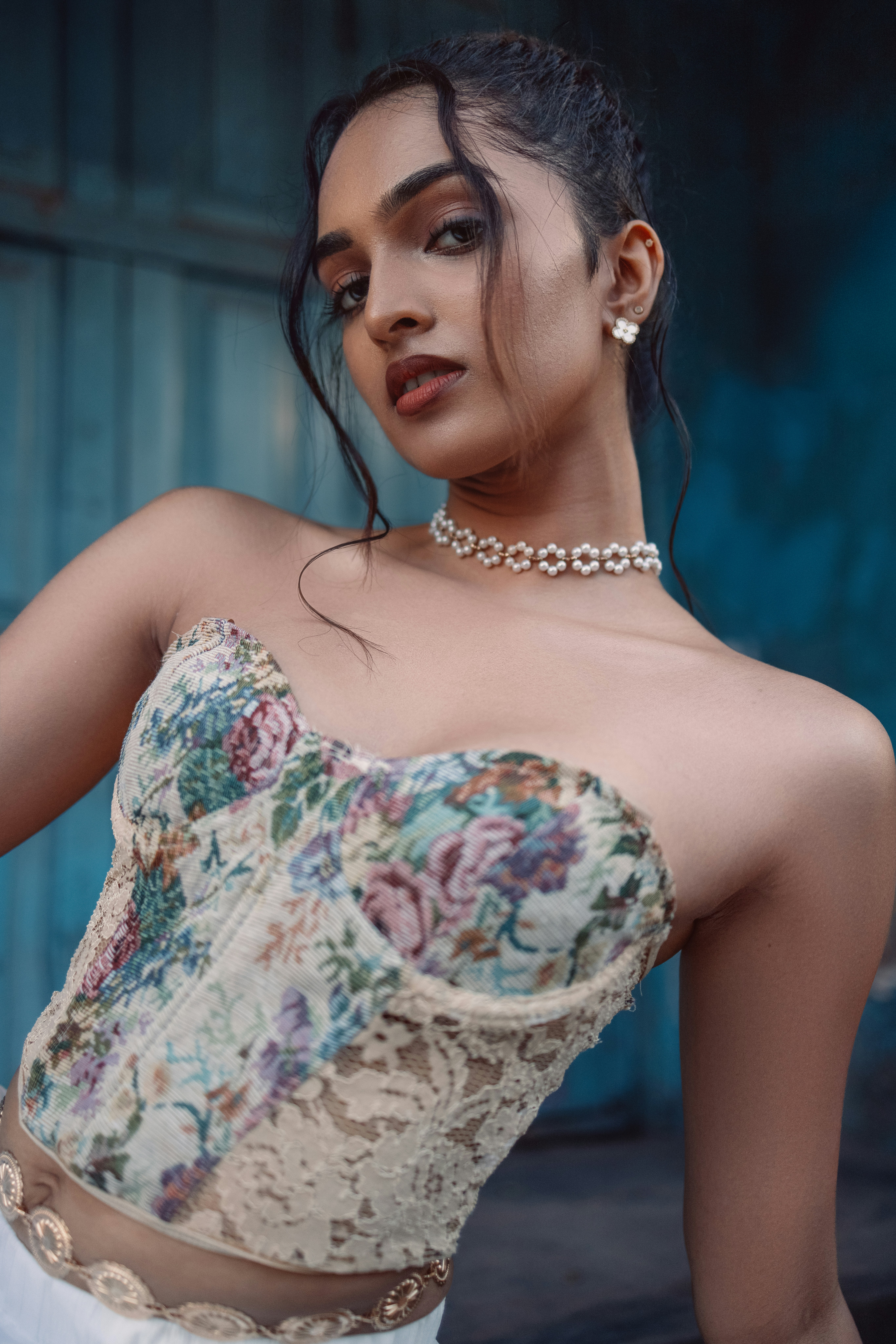 Model showcasing a floral embroidered corset top with intricate lace details, set against a softly blurred blue background.