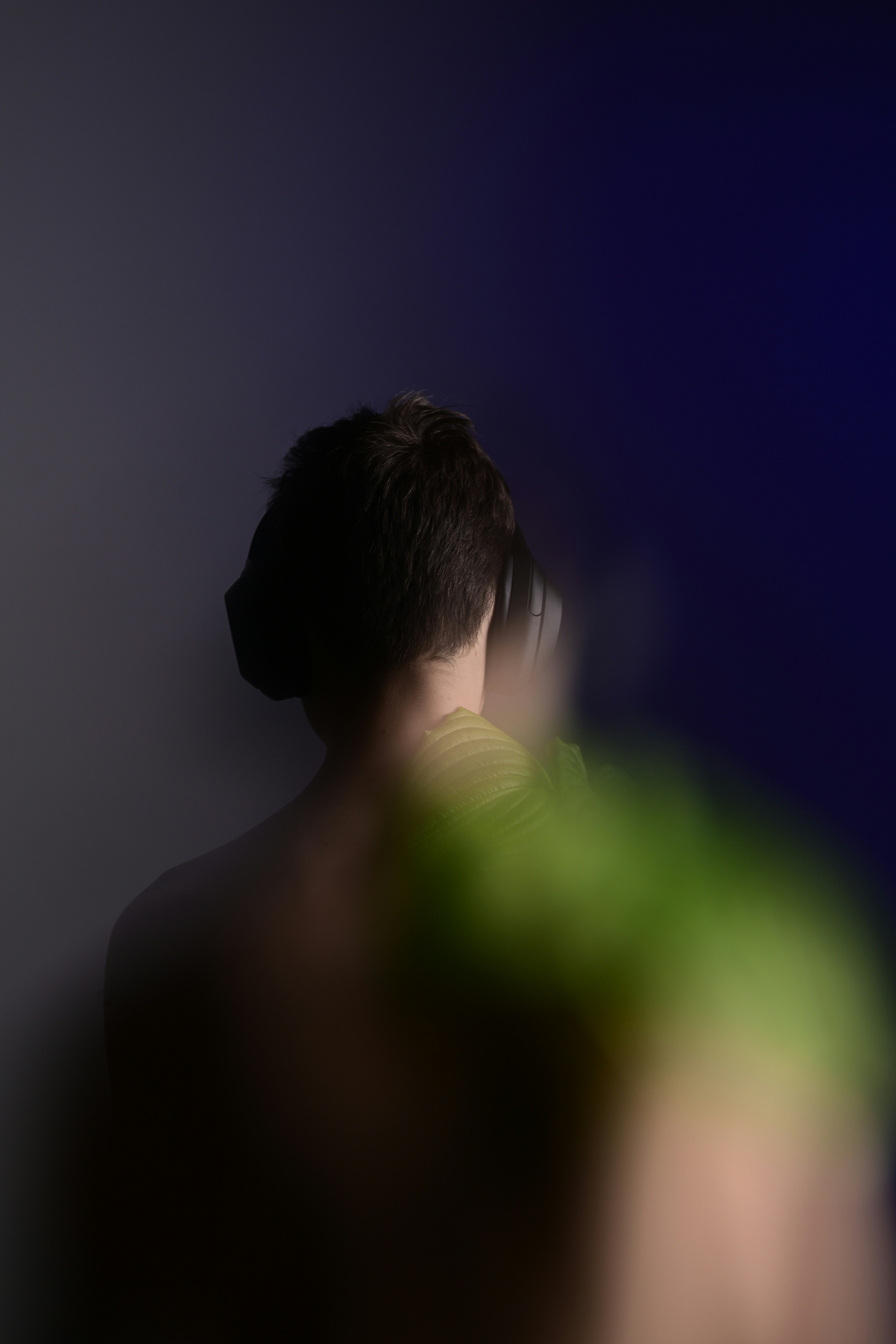 A person wearing headphones, their back turned, immersed in sound, with a blurred green foreground adding depth to the scene.