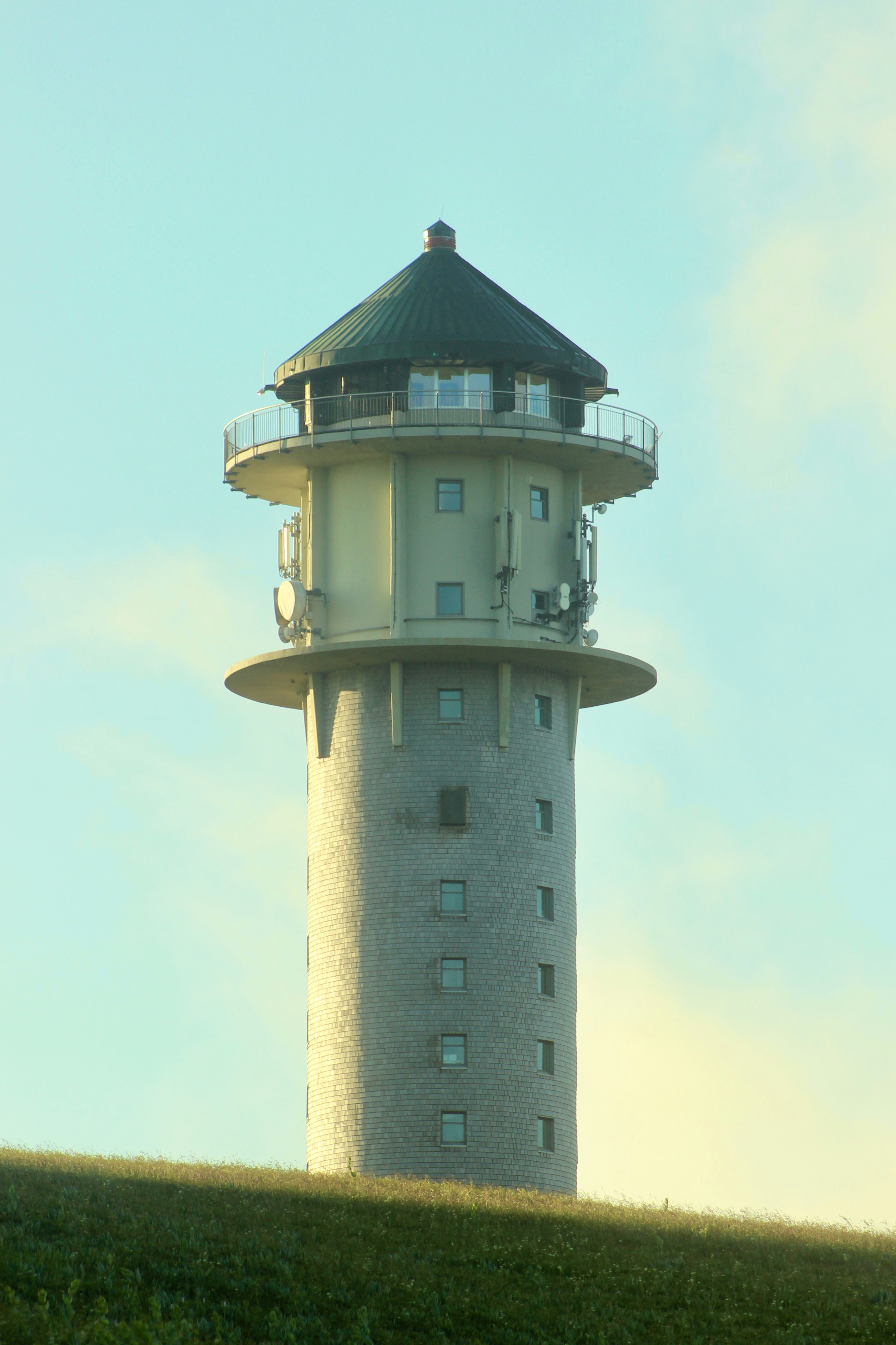 A tall, cylindrical tower with a conical roof, featuring multiple windows and communication equipment, standing proudly against a clear sky.