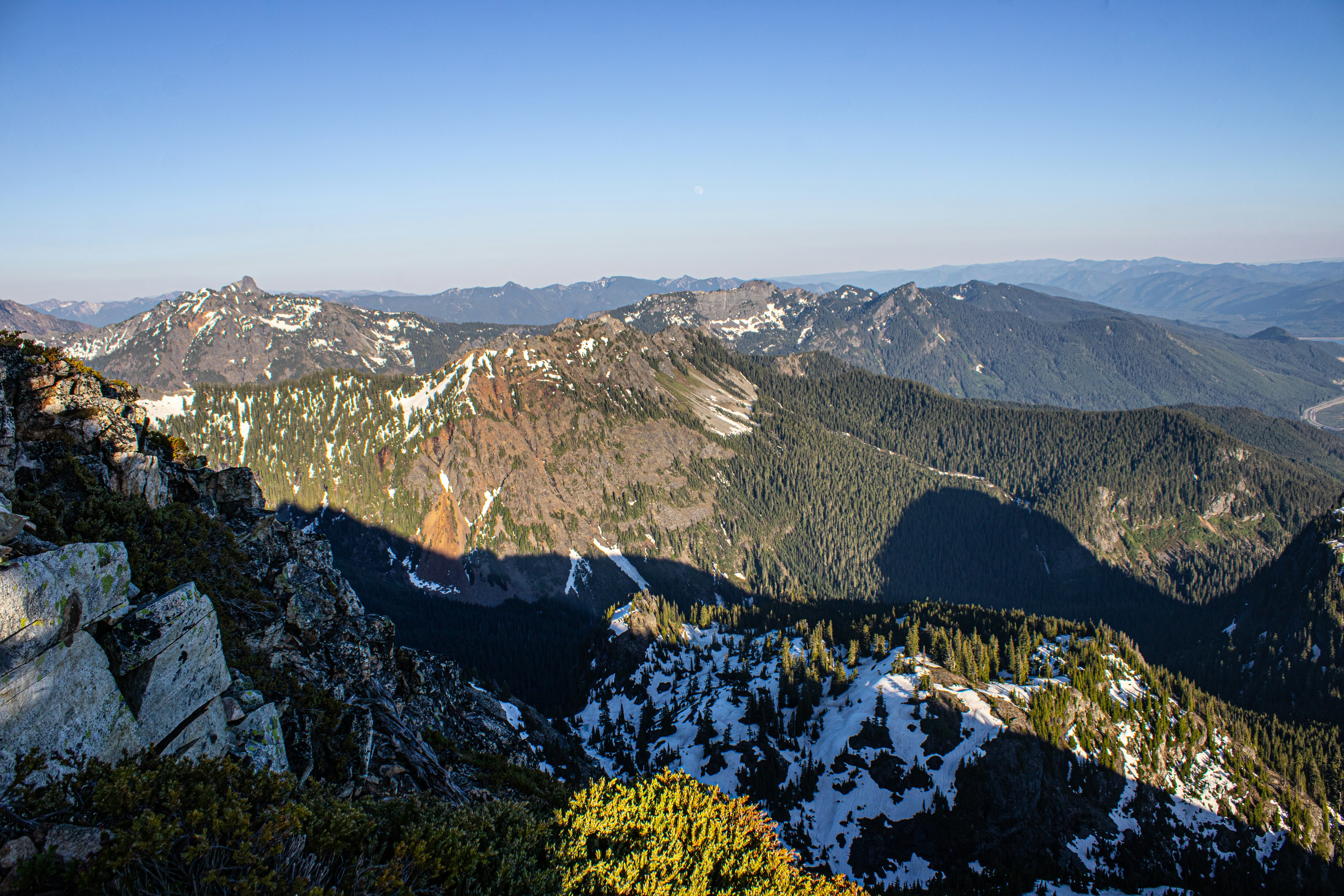 Vast mountain landscape showcasing rugged peaks and patches of snow under a clear sky, emphasizing nature's grandeur.