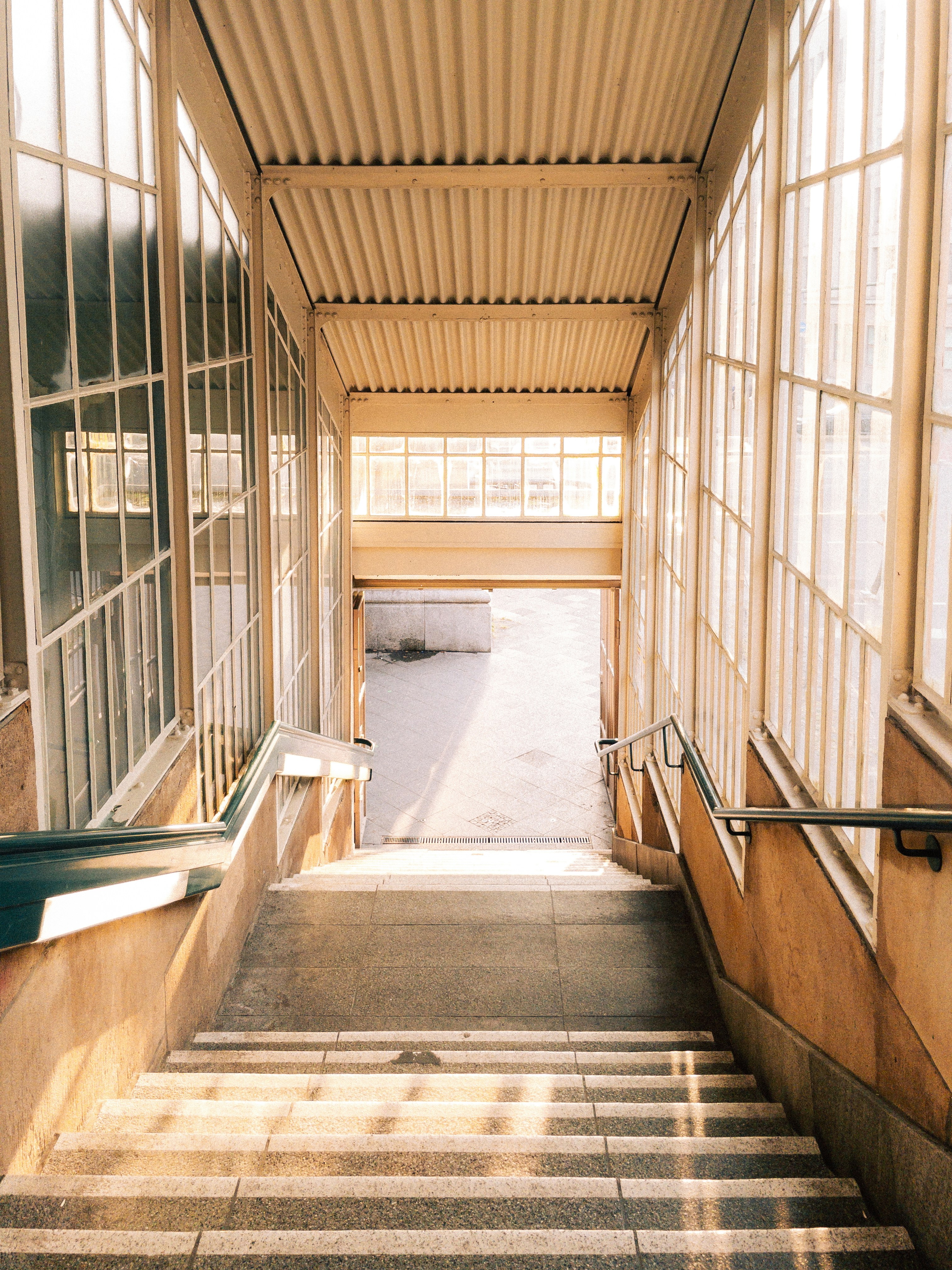 Morning light flooding an old Berlin U-Bahn entrance. The quiet geometry of the glass and steel reflects the charm of the city’s everyday transit spaces — captured in soft, golden tones. | Staircase leading to an open, light-filled area.