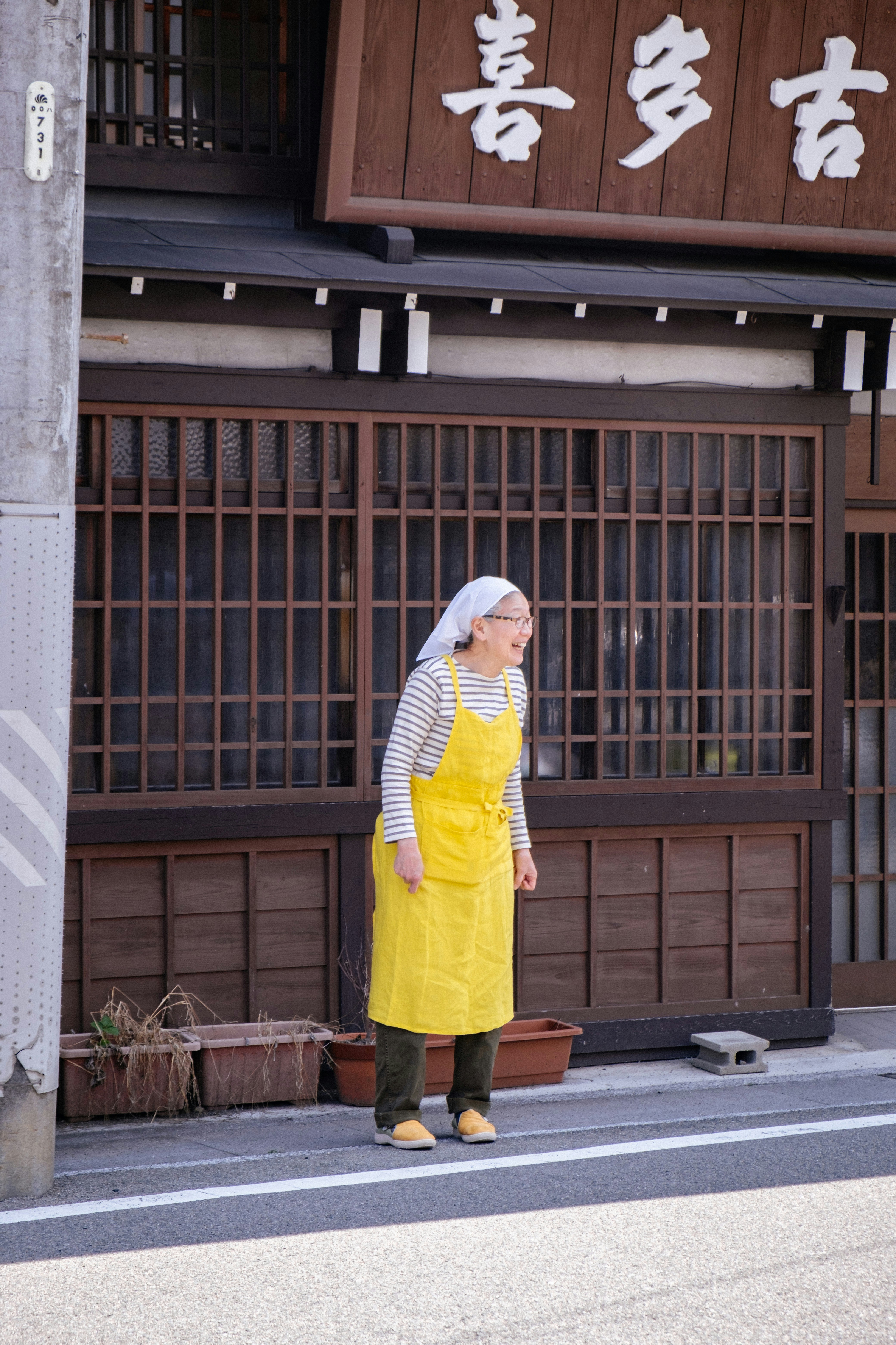 Sunlit Street Portrait: Yellow Apron Before a Traditional Japanese Facade