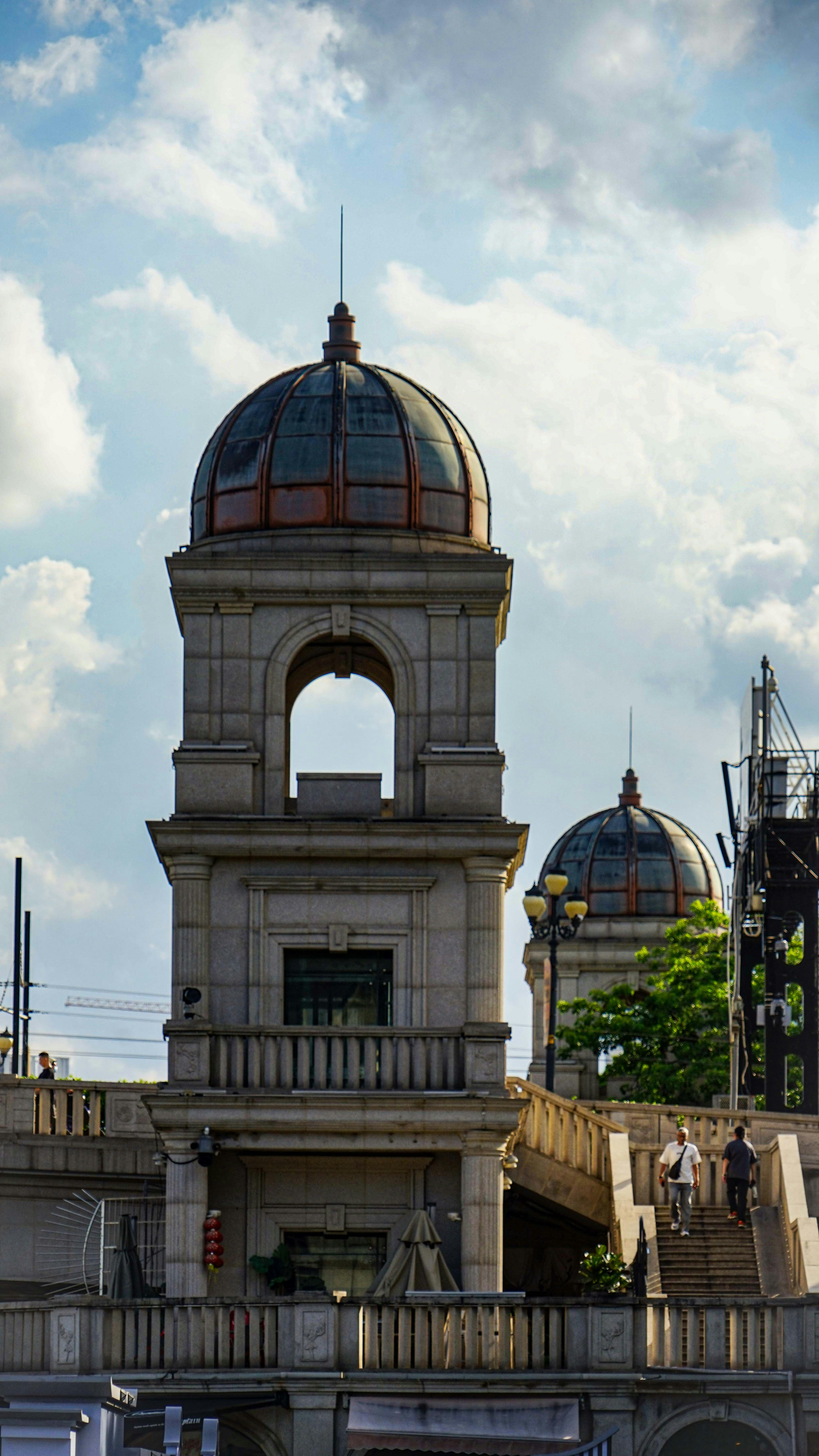 Historic building with domed towers against a backdrop of fluffy clouds and blue sky. The architecture reflects a blend of classic and modern elements.