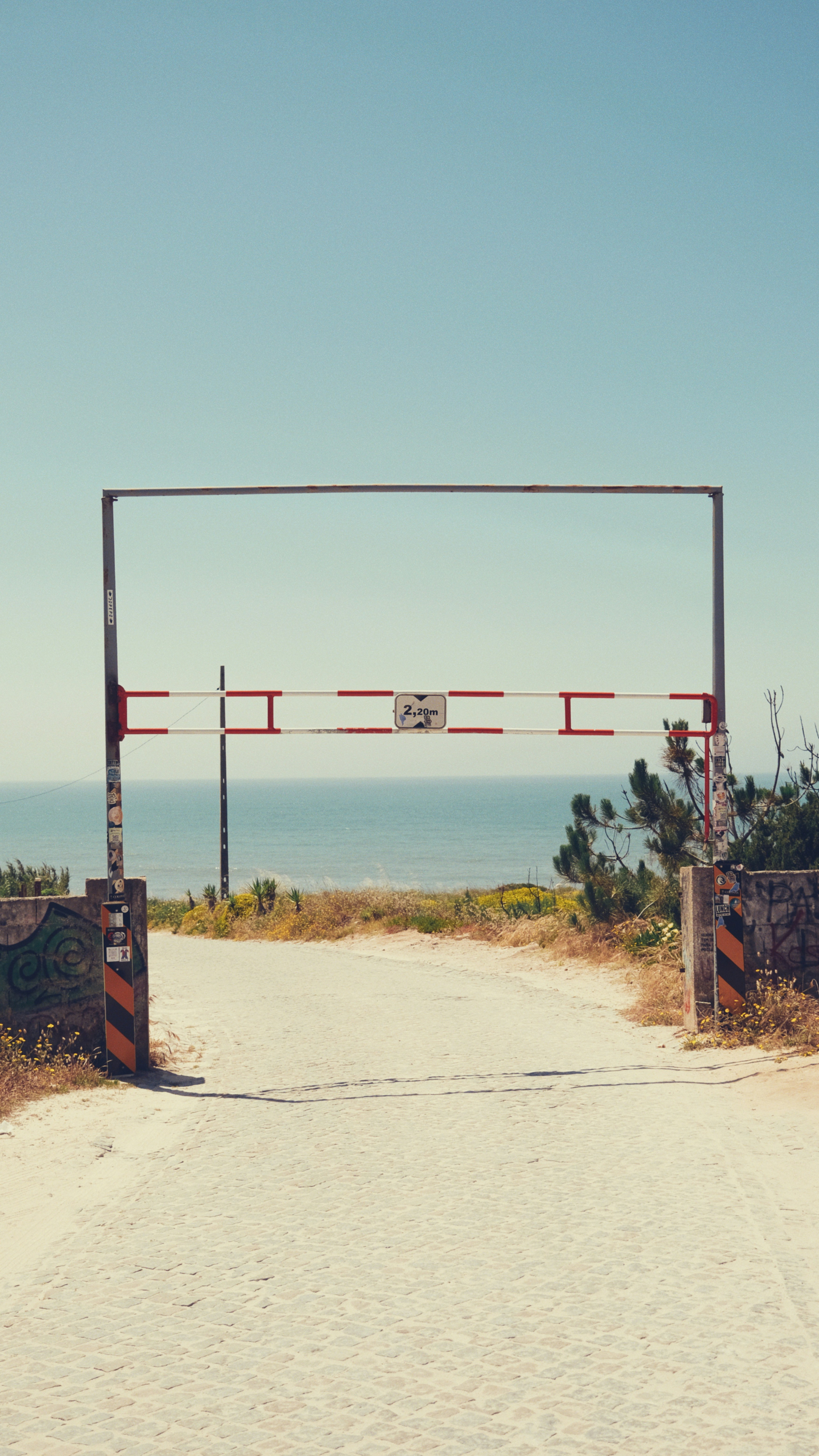 A barrier gate marks the entrance to a coastal path, framed by lush greenery and a serene ocean backdrop.