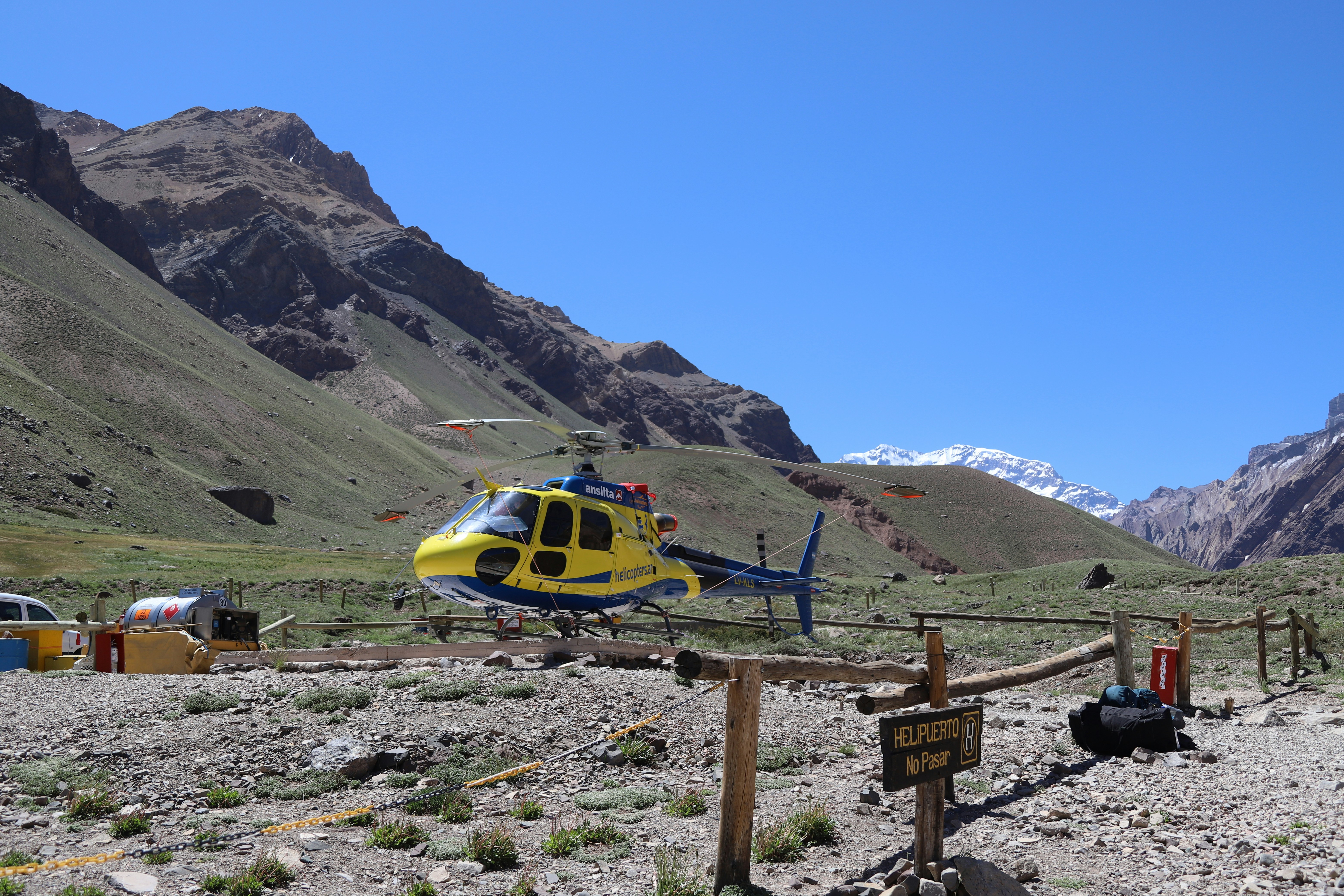 Sunlit Yellow Helicopter on an Alpine Helipad Amid Rugged Peaks
