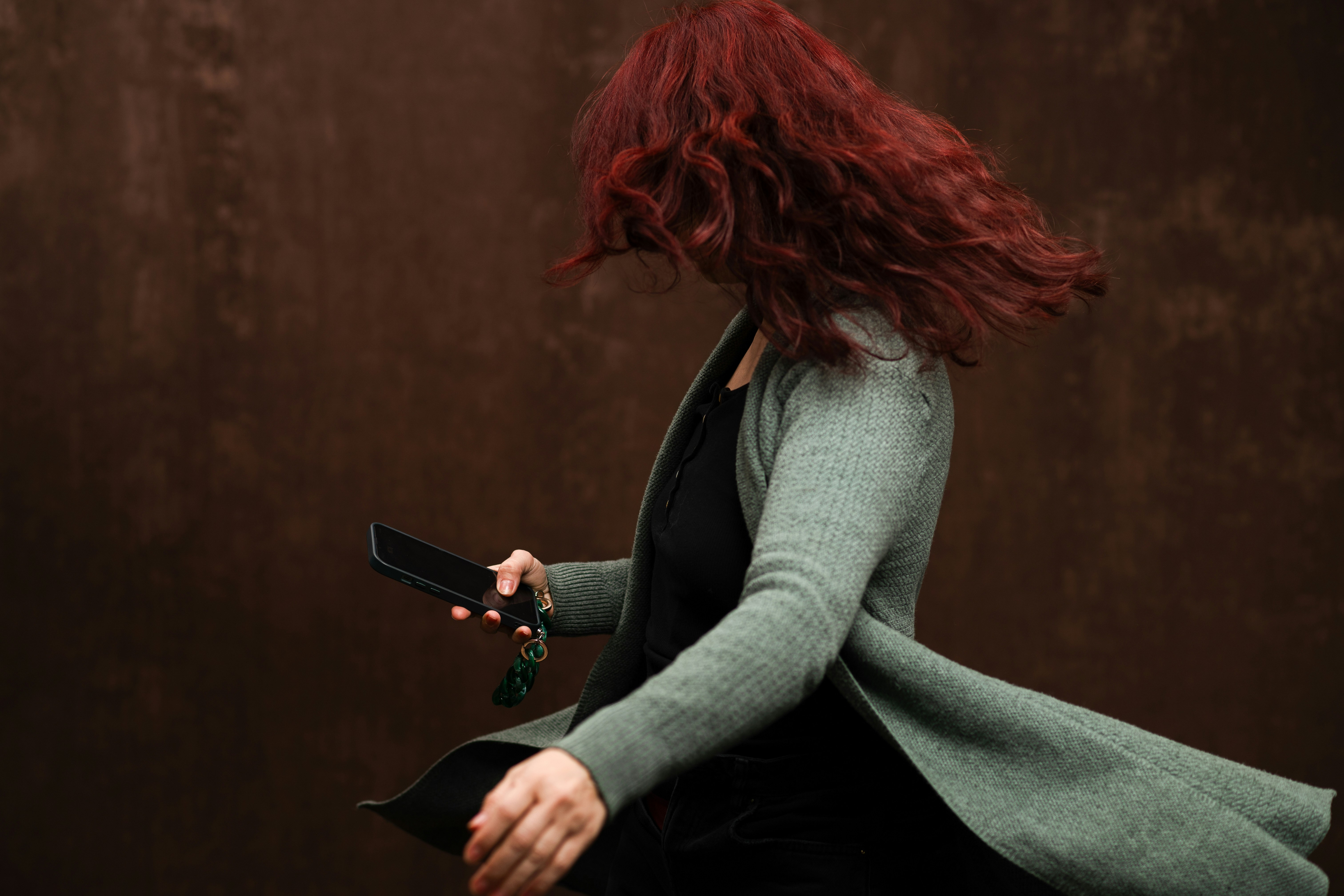 Woman with red hair twirls while holding a phone.