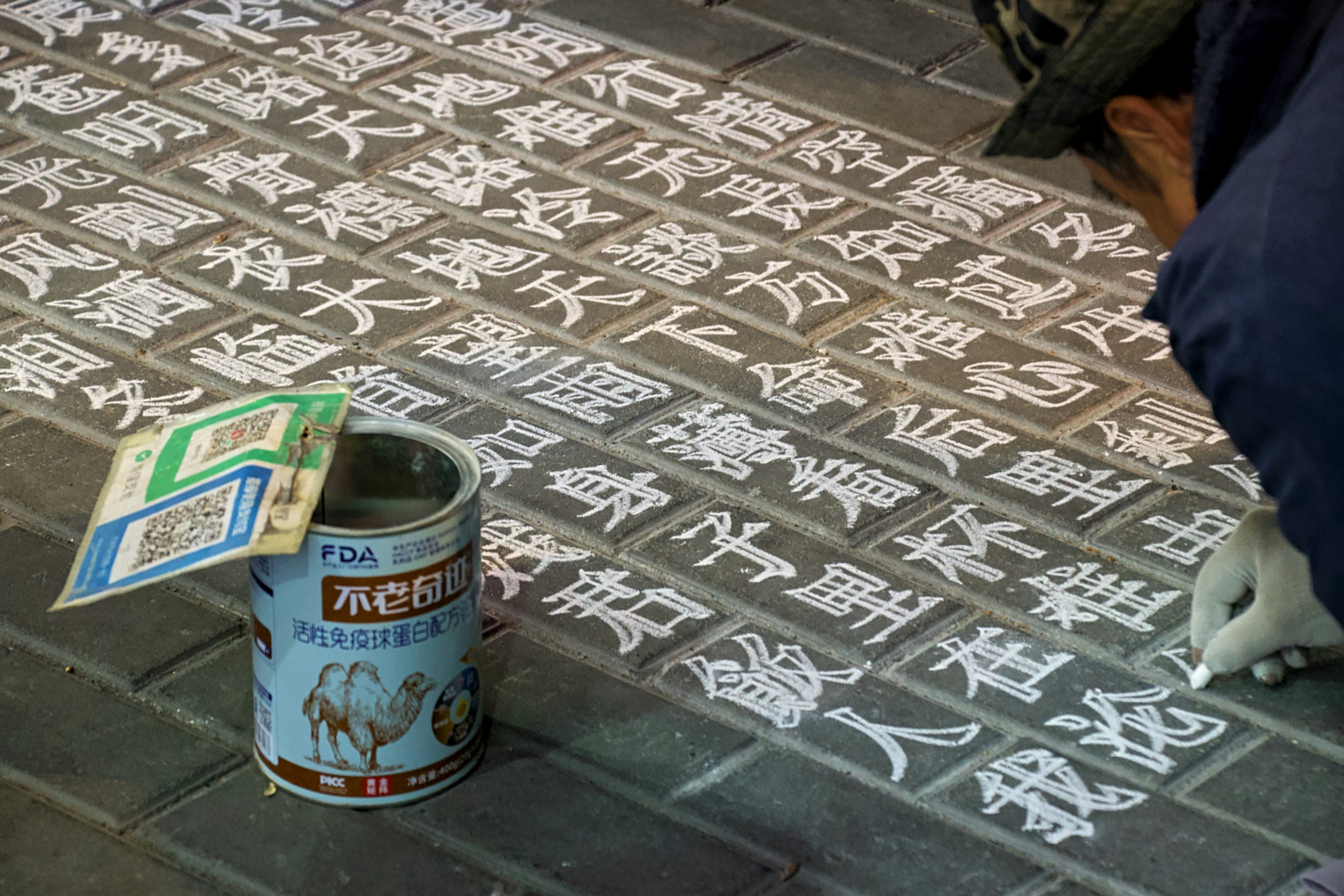 An artist meticulously painting intricate Chinese characters on a brick surface, with a can of paint nearby, showcasing the beauty of street art.