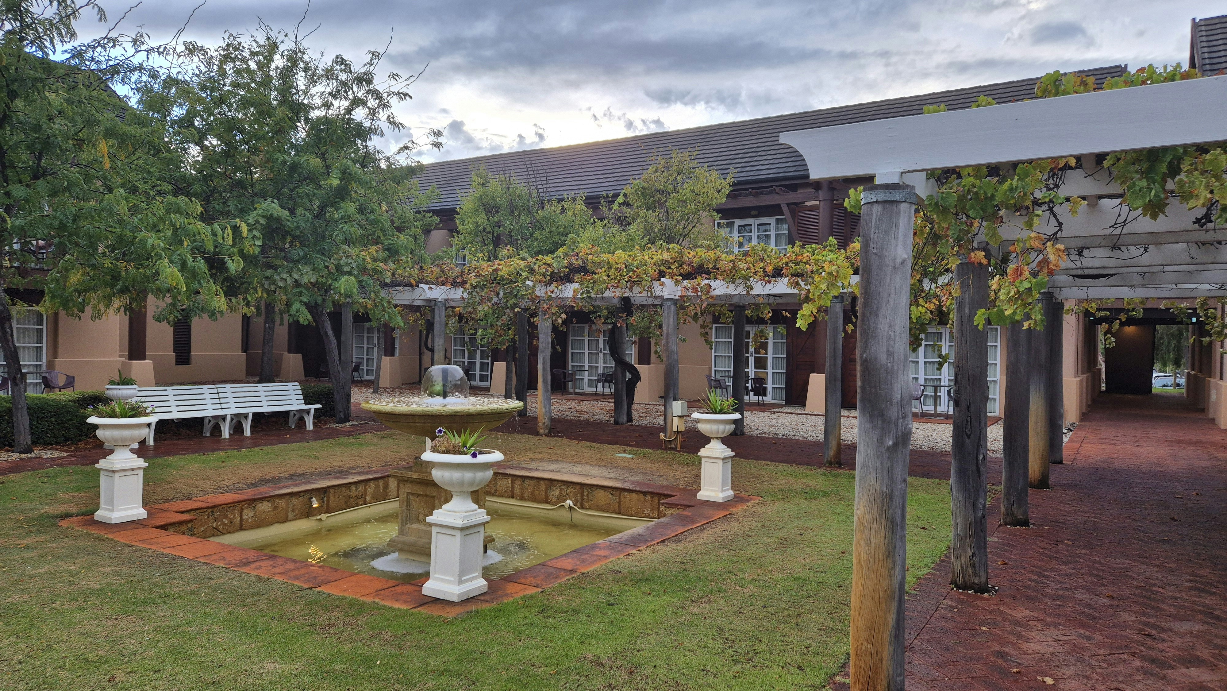 Centerpiece Calm: Fountain Under Vine-Lined Arbors in a Courtyard